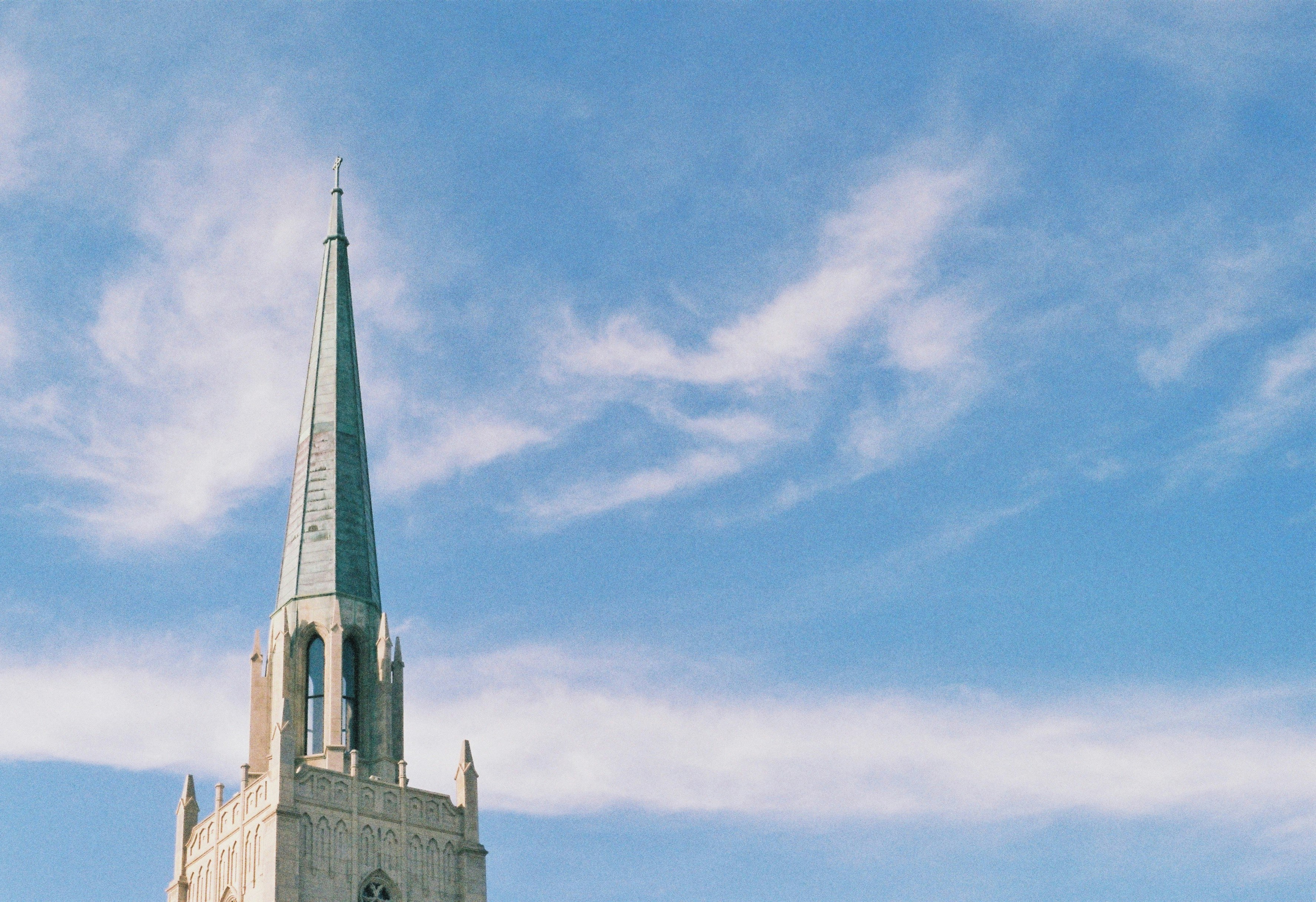 Church steeple reaching towards wispy clouds in a bright blue sky.