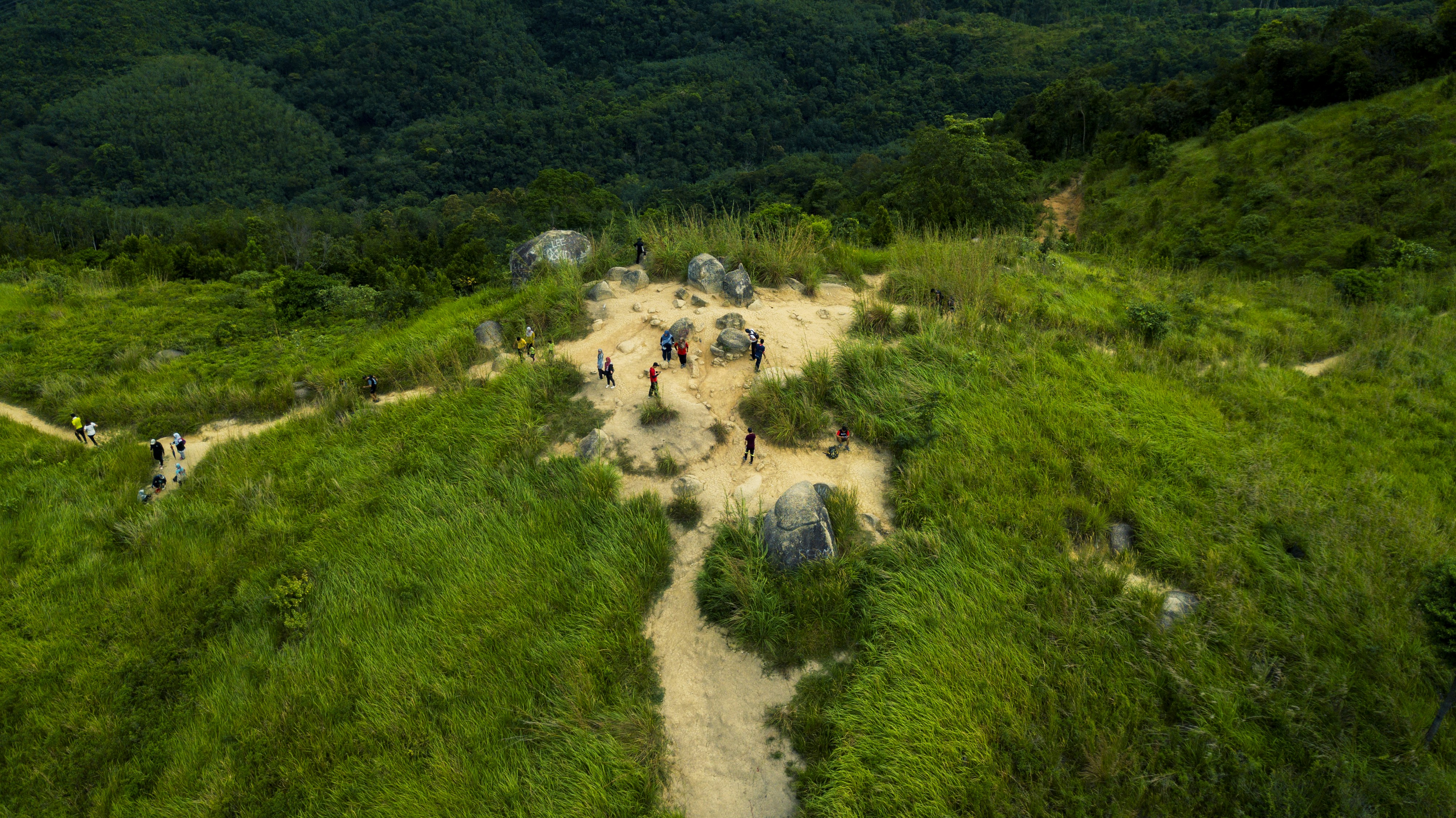 Aerial view of hikers navigating rocky trails amidst lush greenery on Bukit Broga's peak.