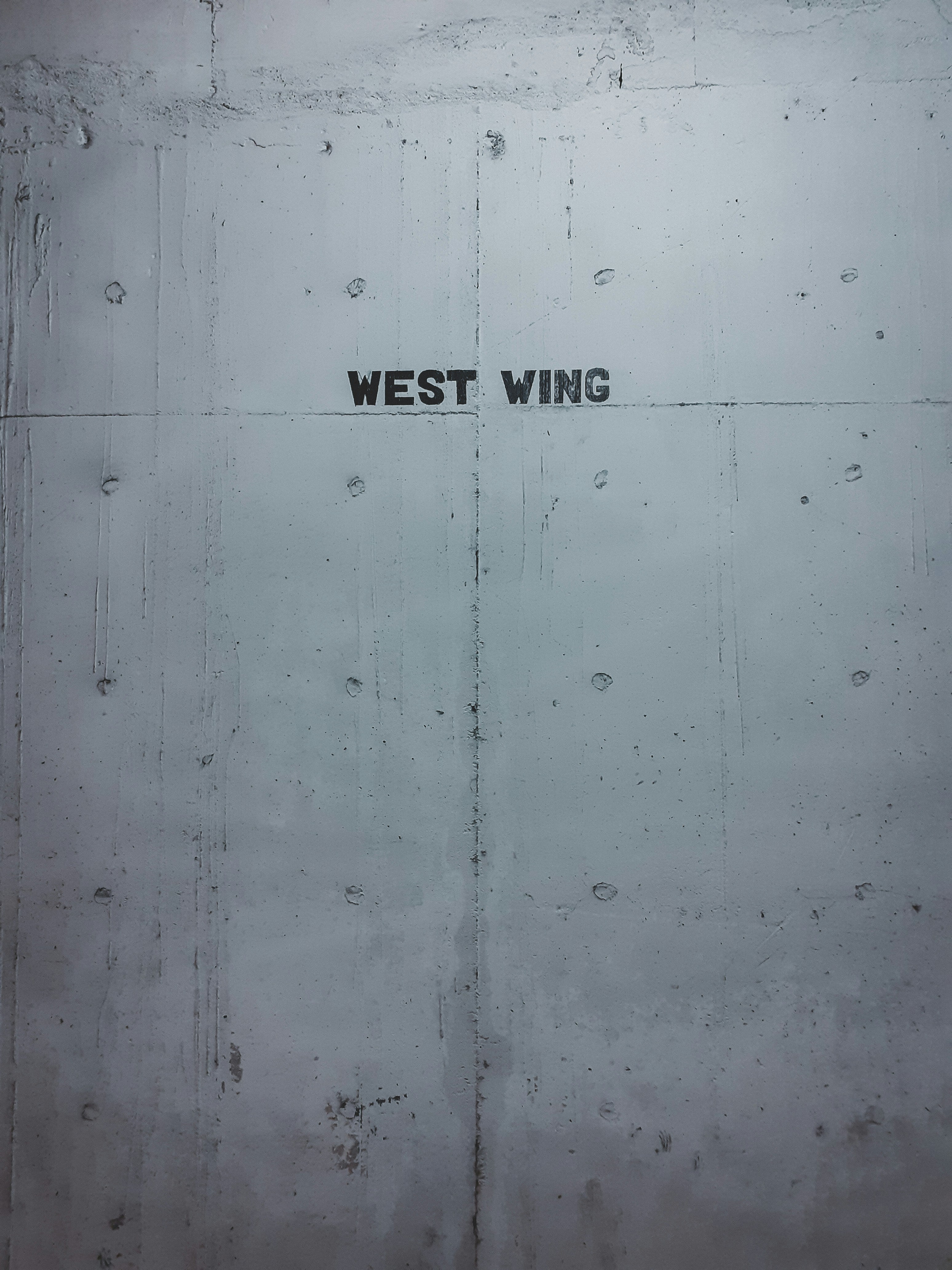Bold lettering 'WEST WING' on a textured concrete wall, emphasizing industrial aesthetics. The stark contrast highlights the minimalist design.