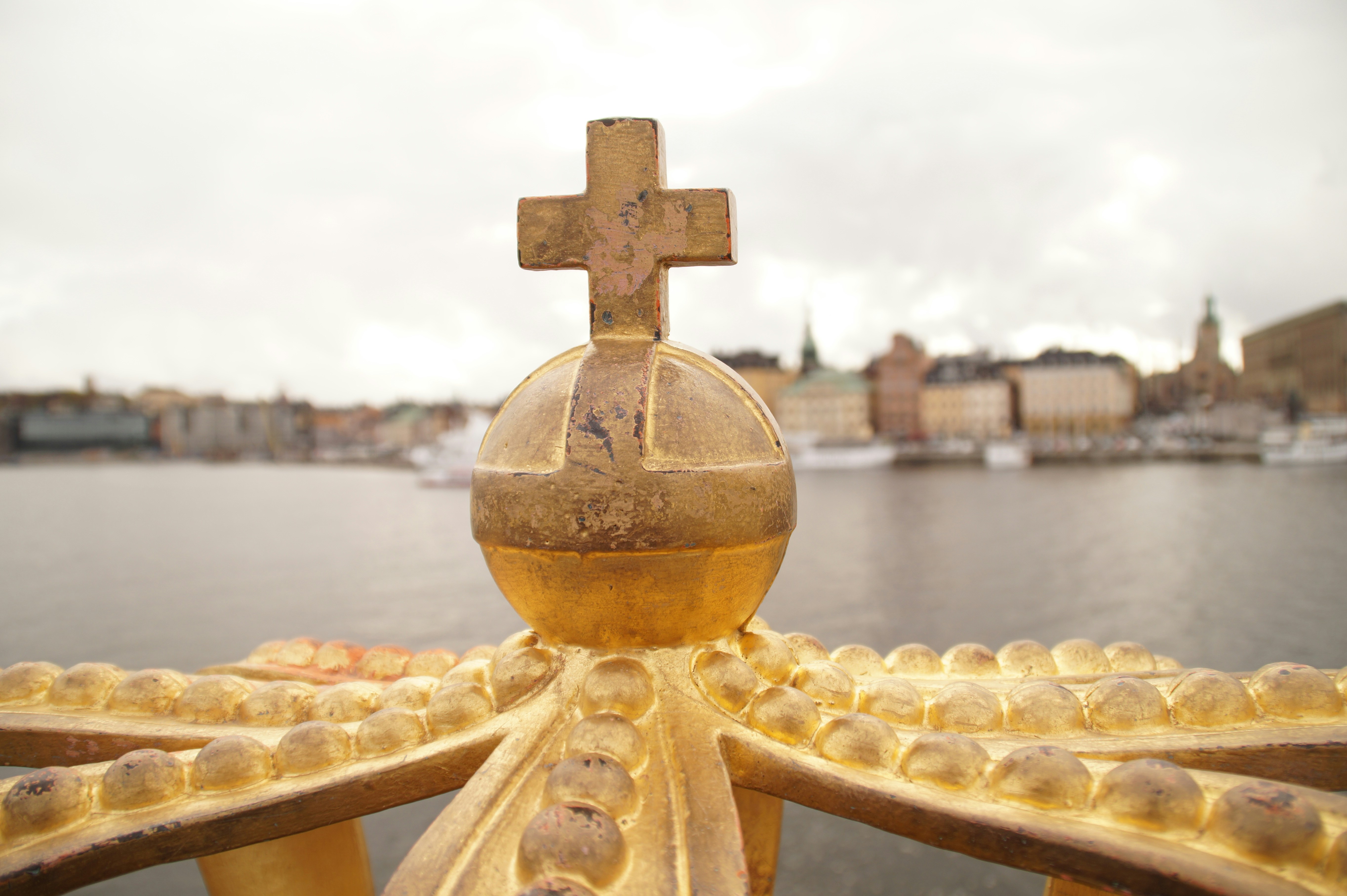 Golden cross atop a domed sphere overlooking a distant cityscape by the river