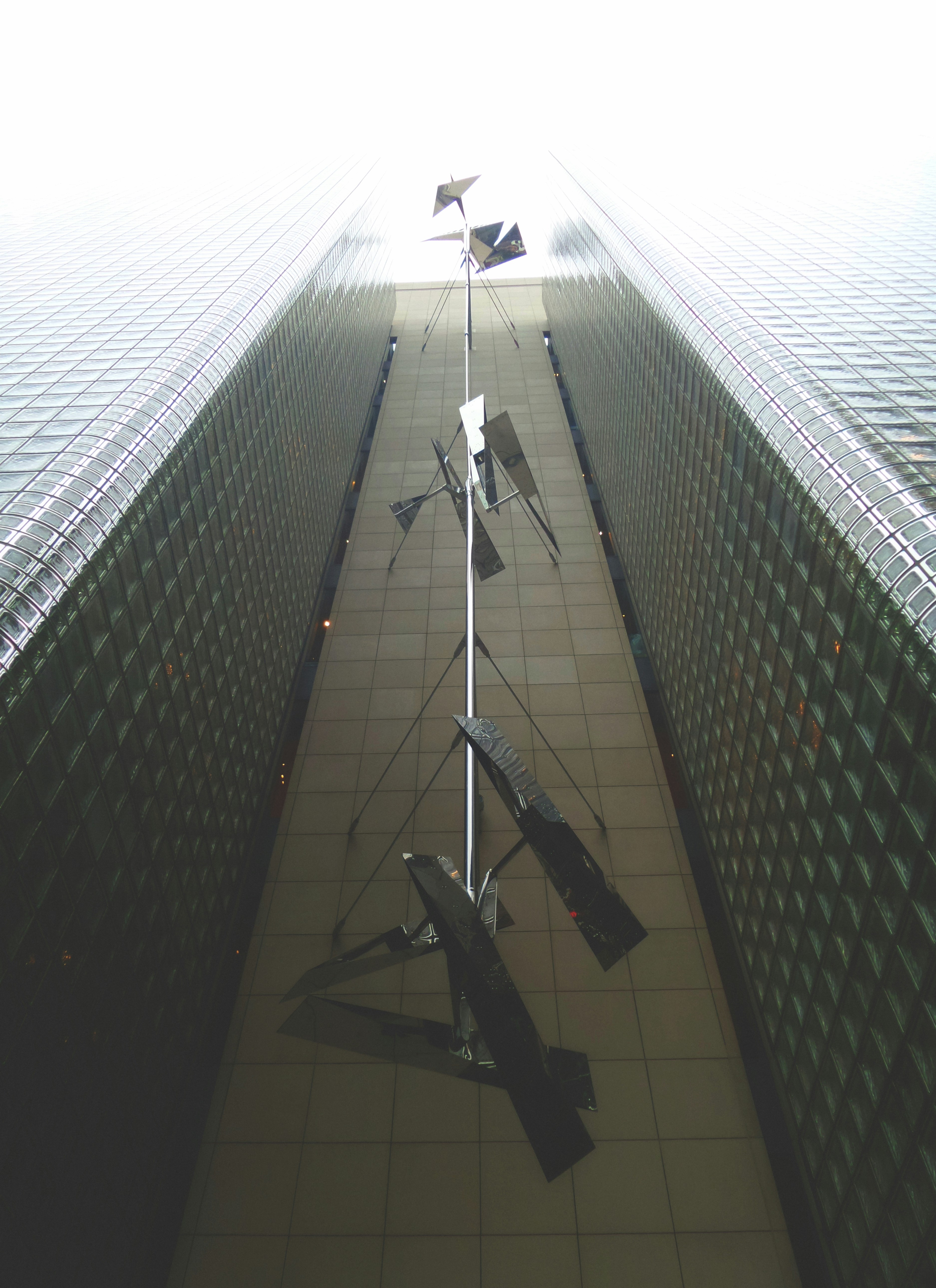 Sculptural installation suspended between glass skyscrapers, viewed from below, highlighting the interplay of architecture and art.
