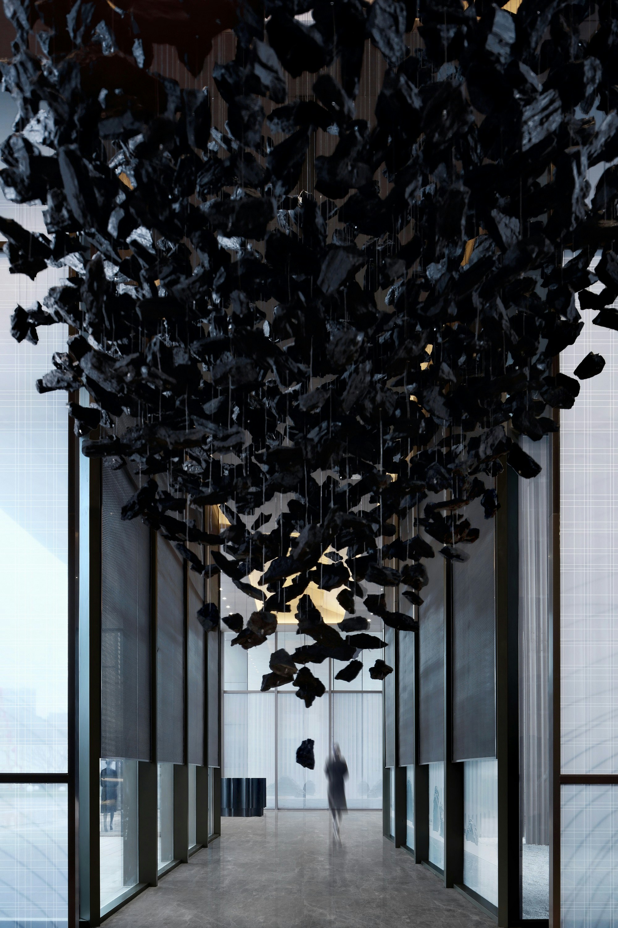 A person walking down a long hallway with lots of black objects hanging ...