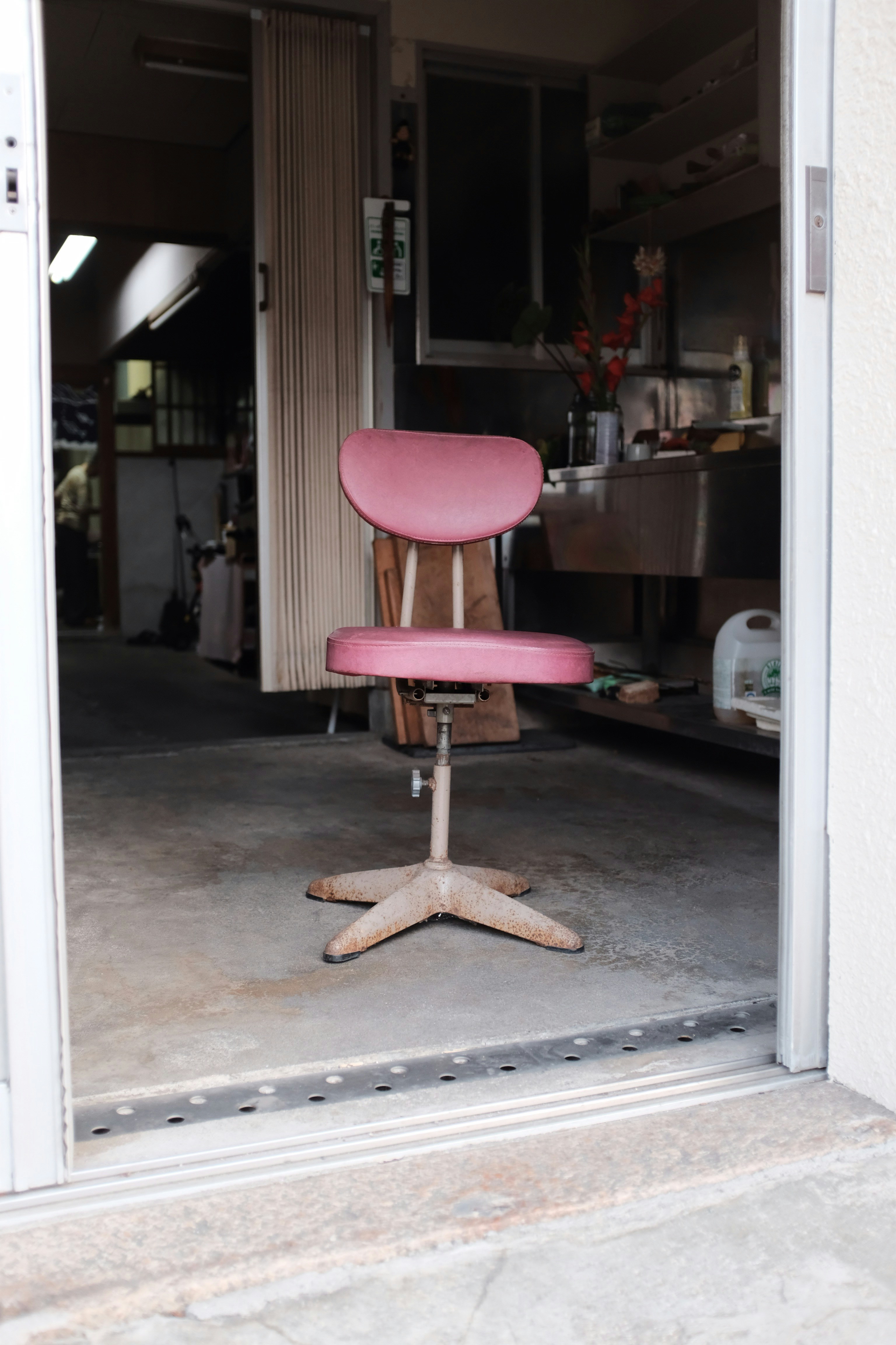 Pastel Perch: A Pink Chair Stands Ground in a Workshop Doorway