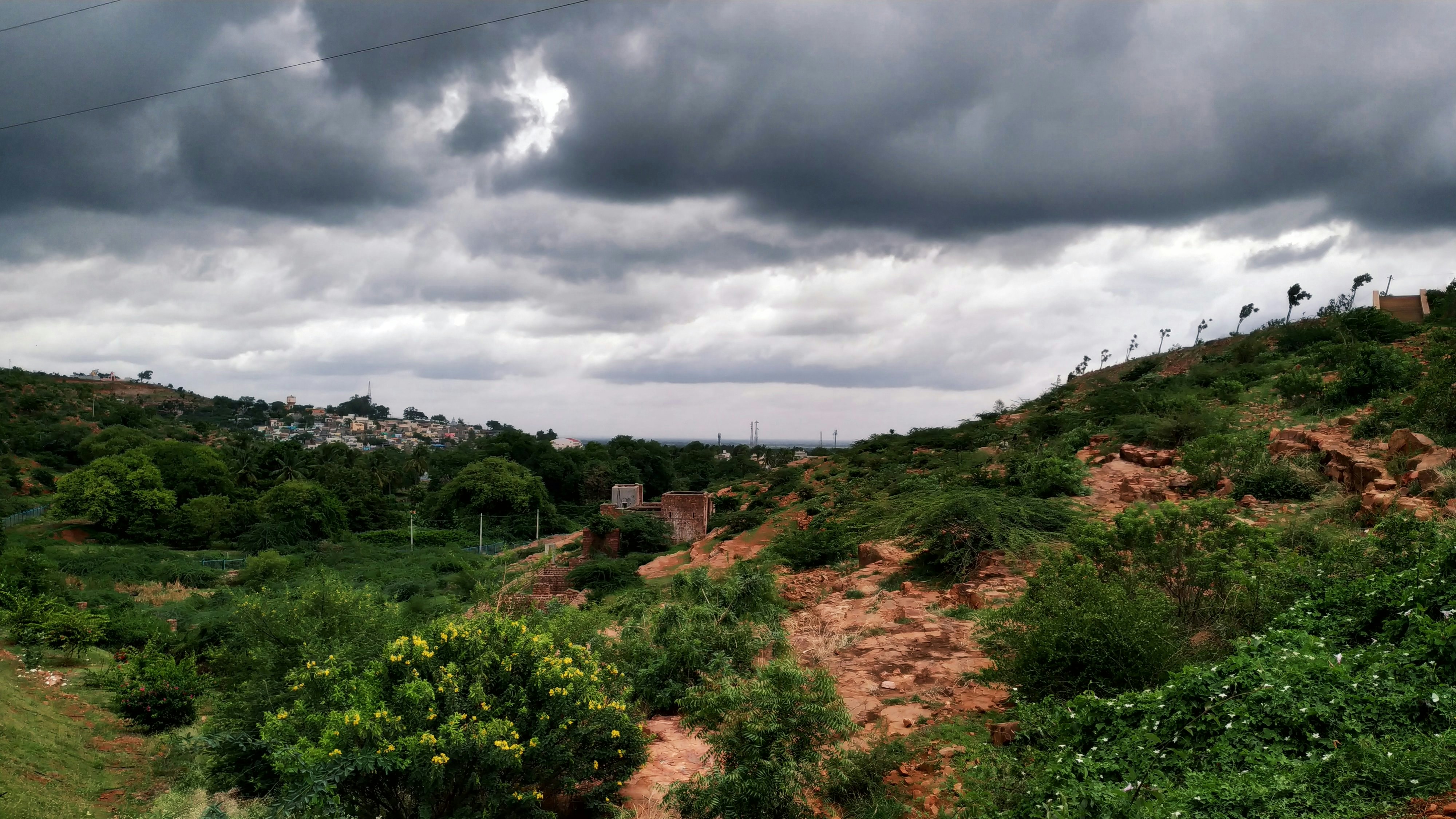 Dramatic clouds loom over lush green hills and scattered shrubs, hinting at an approaching storm.