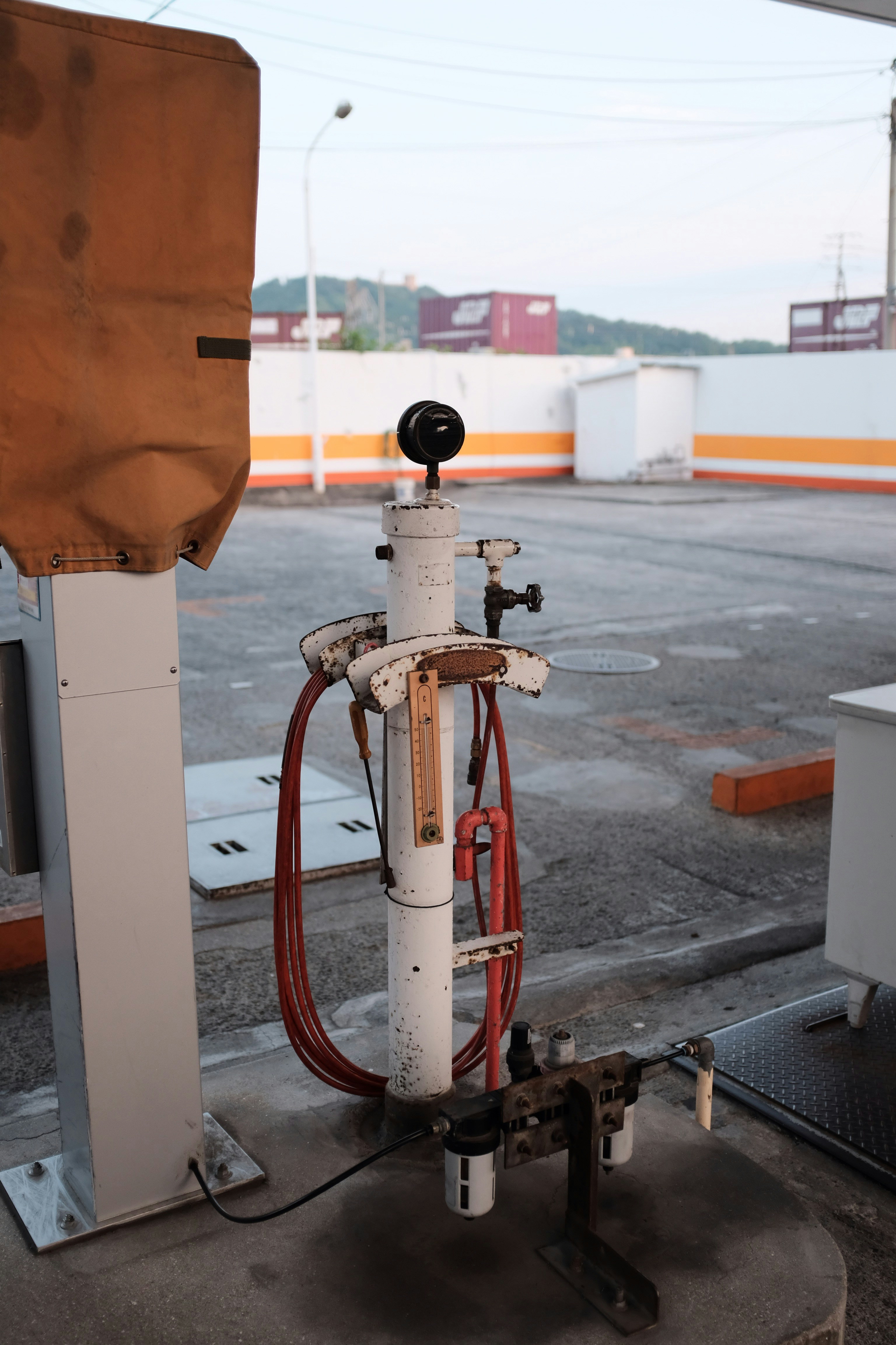 An old fuel pump surrounded by industrial elements, showcasing wear and neglect in an urban setting.