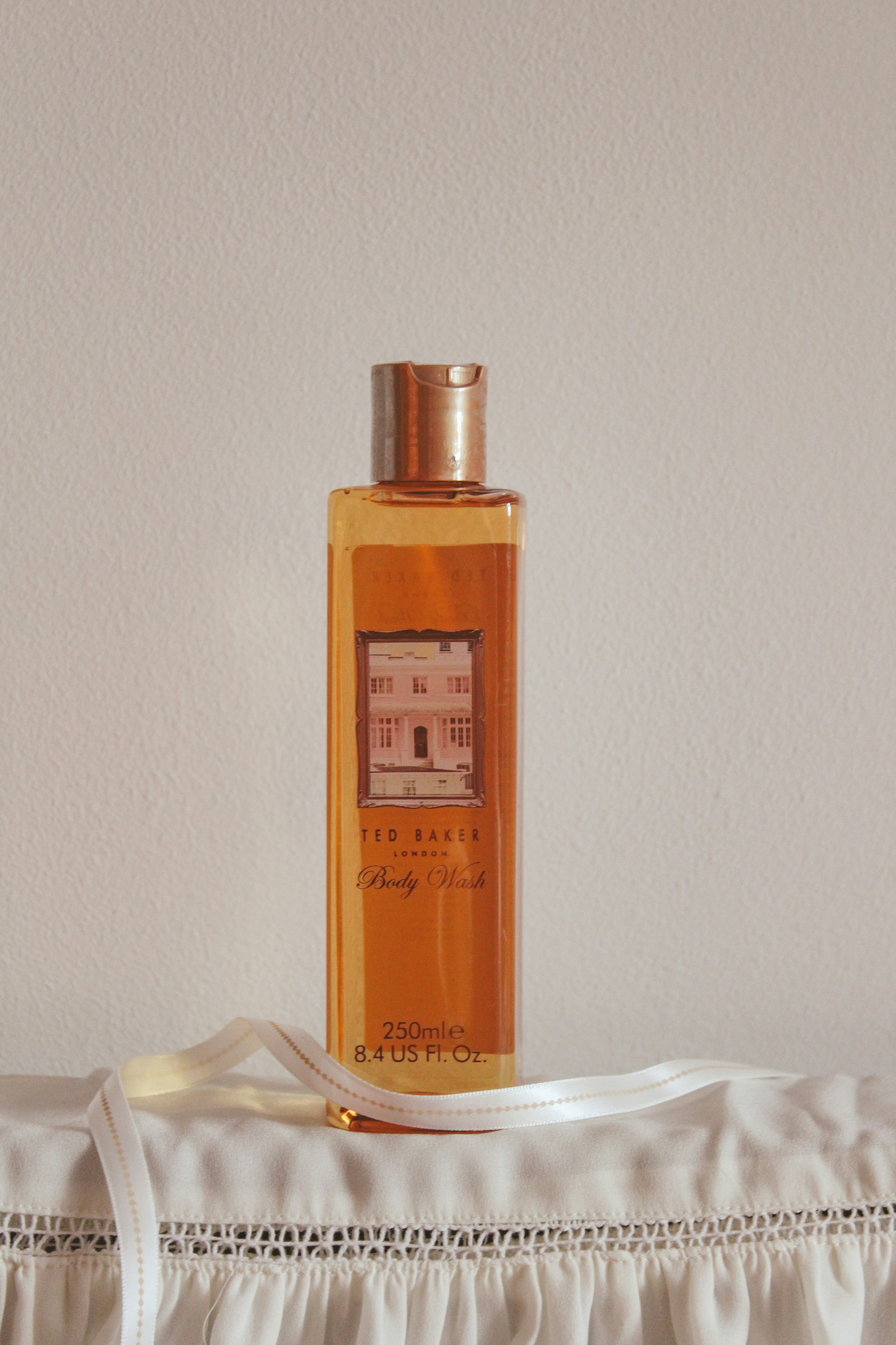 A bottle of Ted Baker body wash sits elegantly on a textured surface, showcasing its refined design and amber liquid. The soft lighting enhances the product's luxurious appeal.