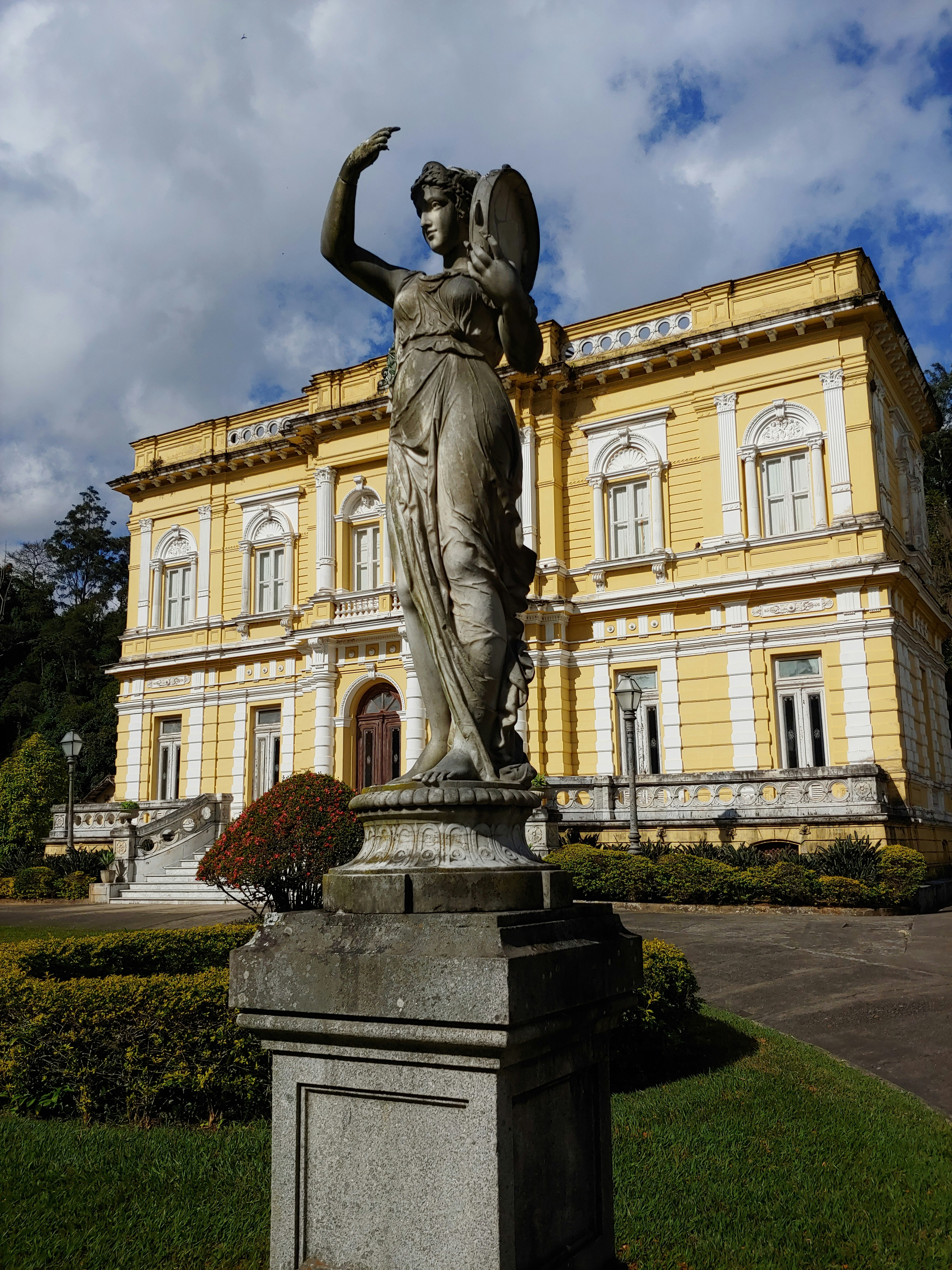 Stone statue in front of a historic yellow manor under a partly cloudy sky.