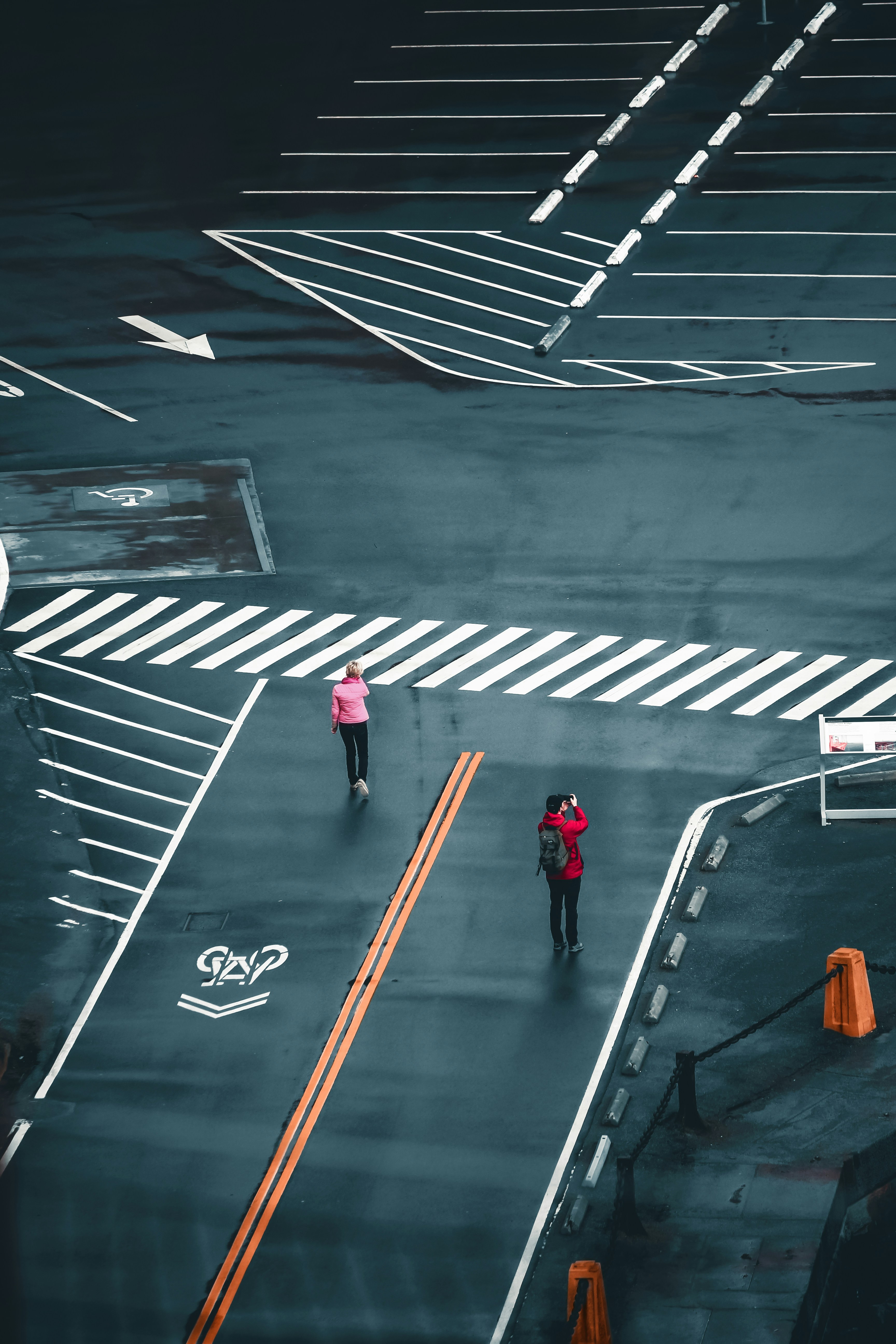Two figures navigating a deserted parking lot, surrounded by stark lines and patterns of asphalt. The scene captures a blend of solitude and urban life.
