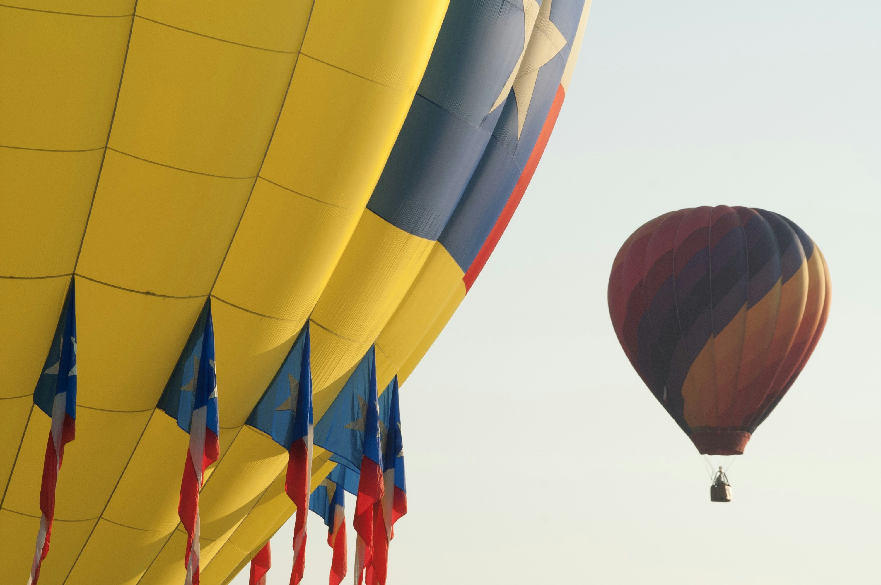 Two hot air balloons in vibrant colors drift gently across a clear sky.