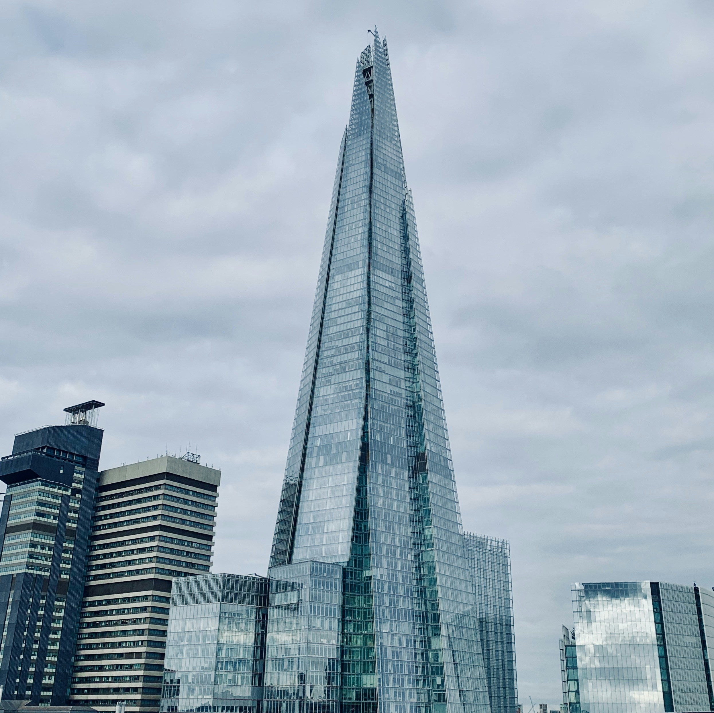Sleek glass skyscraper towering above surrounding buildings under a cloudy sky.