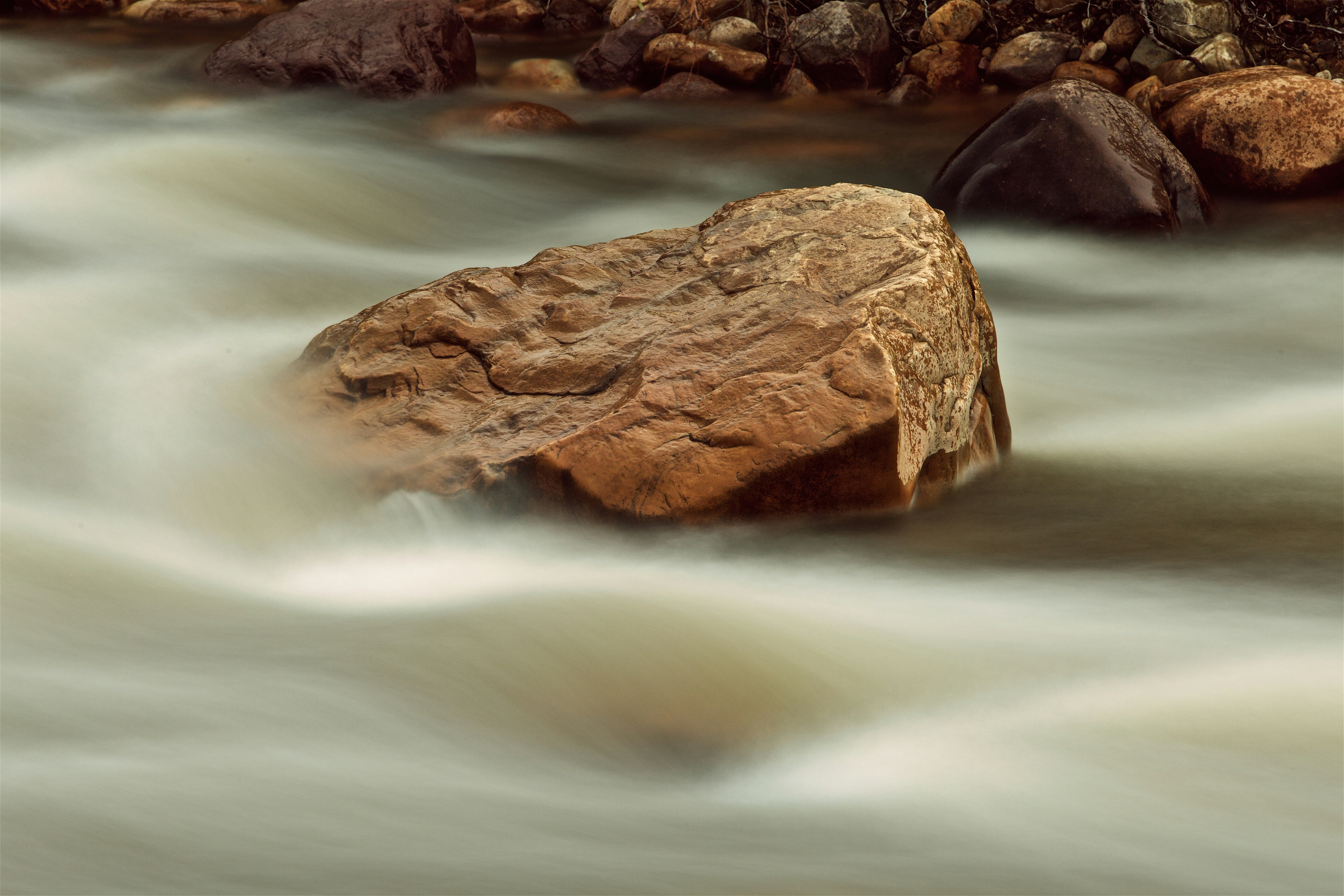 Smooth flowing river around a solitary rock, creating a misty effect in gentle motion.