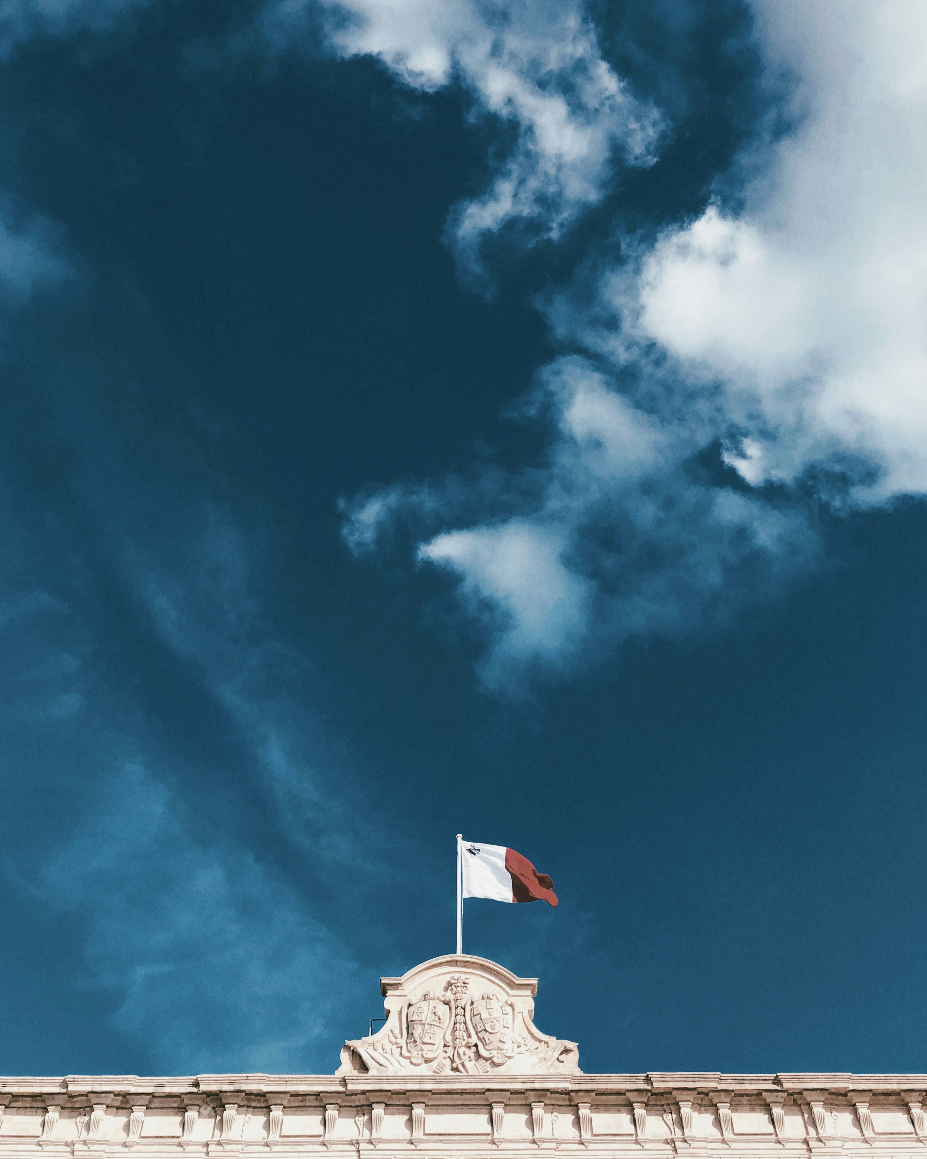 A flag proudly waves atop a historic building under a vast blue sky adorned with wispy clouds.
