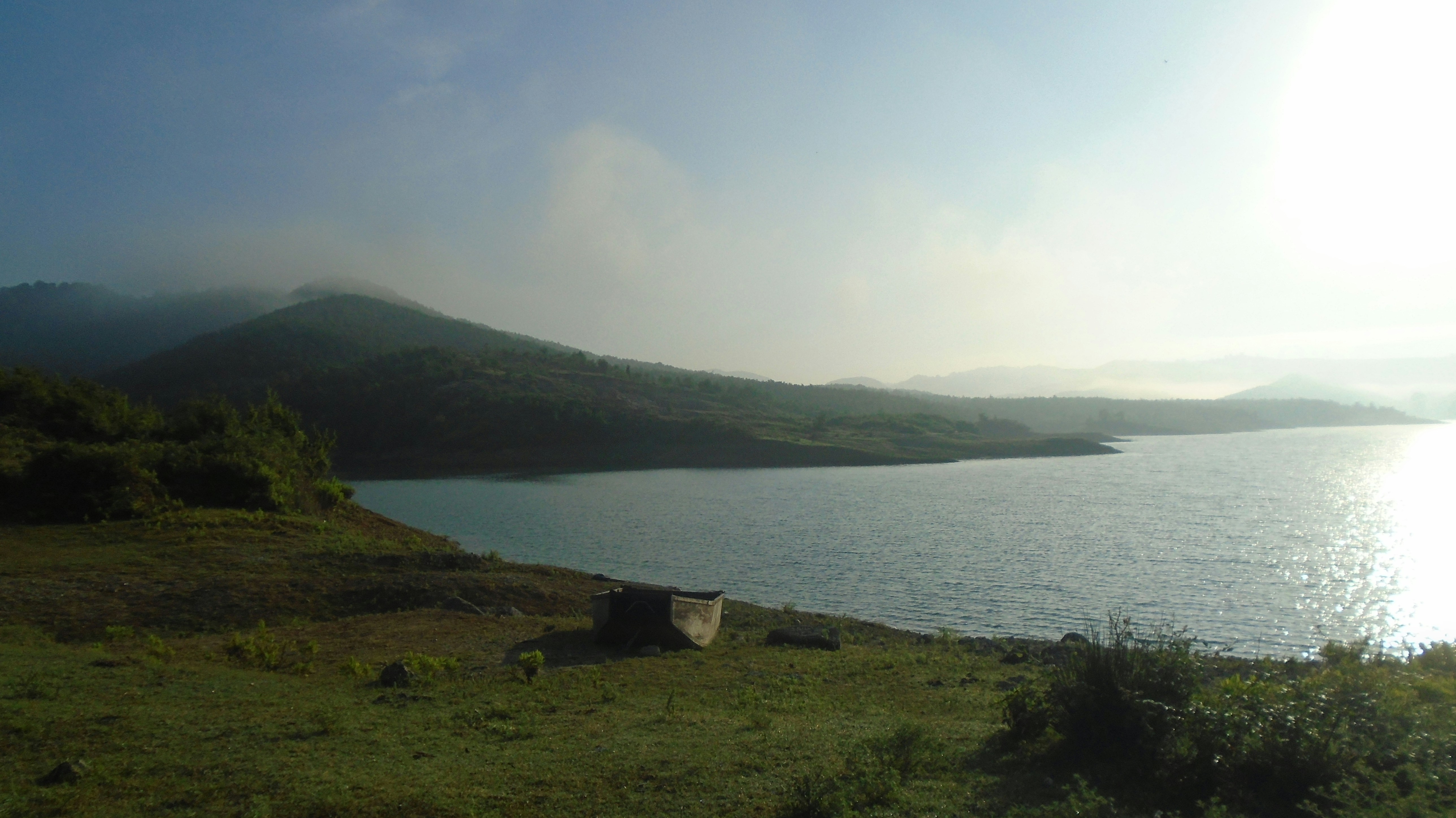 Serene landscape featuring a tranquil lake bordered by gentle hills under a soft morning haze. A lone boat rests on the shore, inviting exploration.