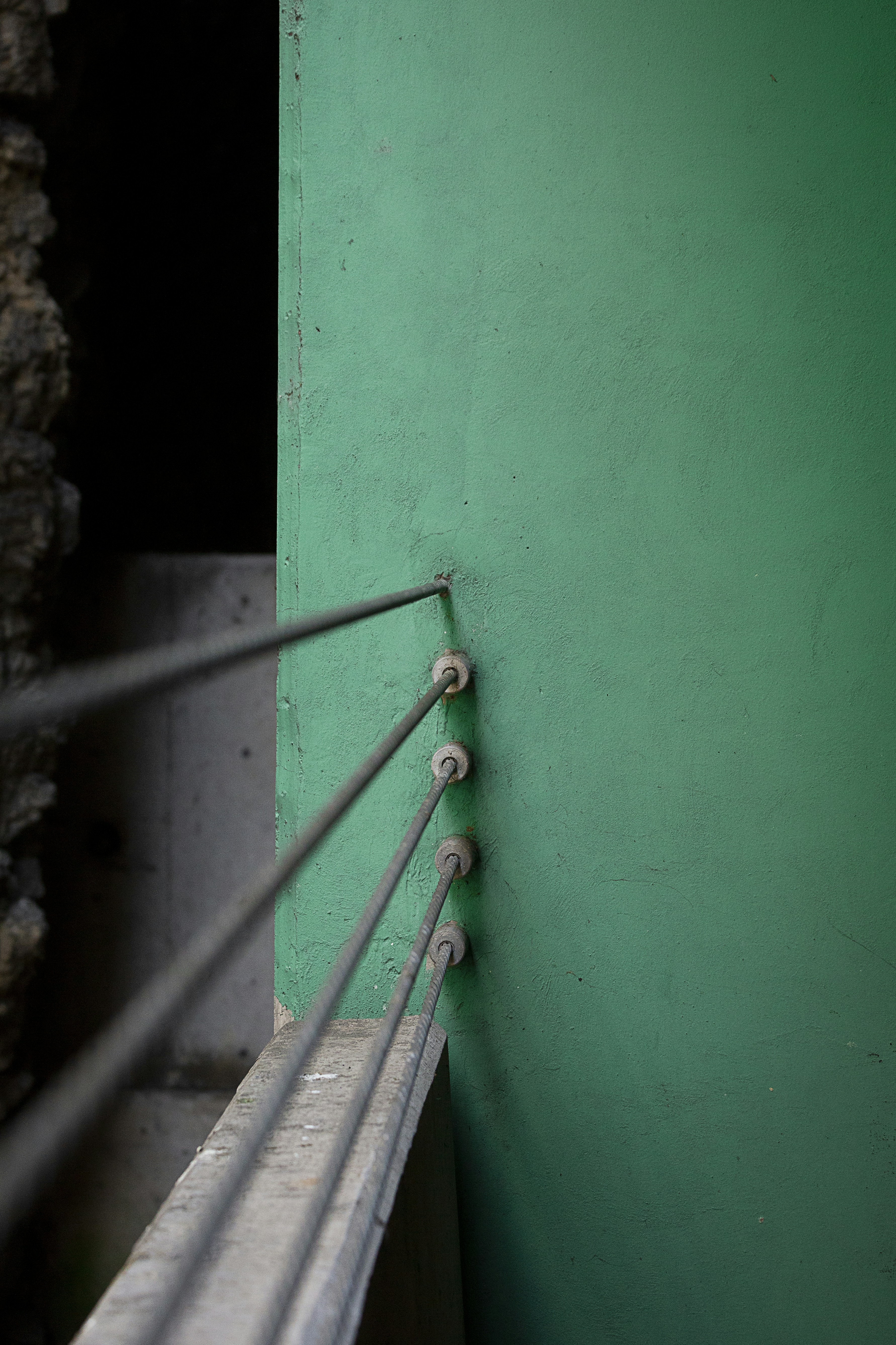 Close-up of steel cables anchored to a vibrant green wall, showcasing the interplay of industrial materials and color. The composition emphasizes depth and perspective.