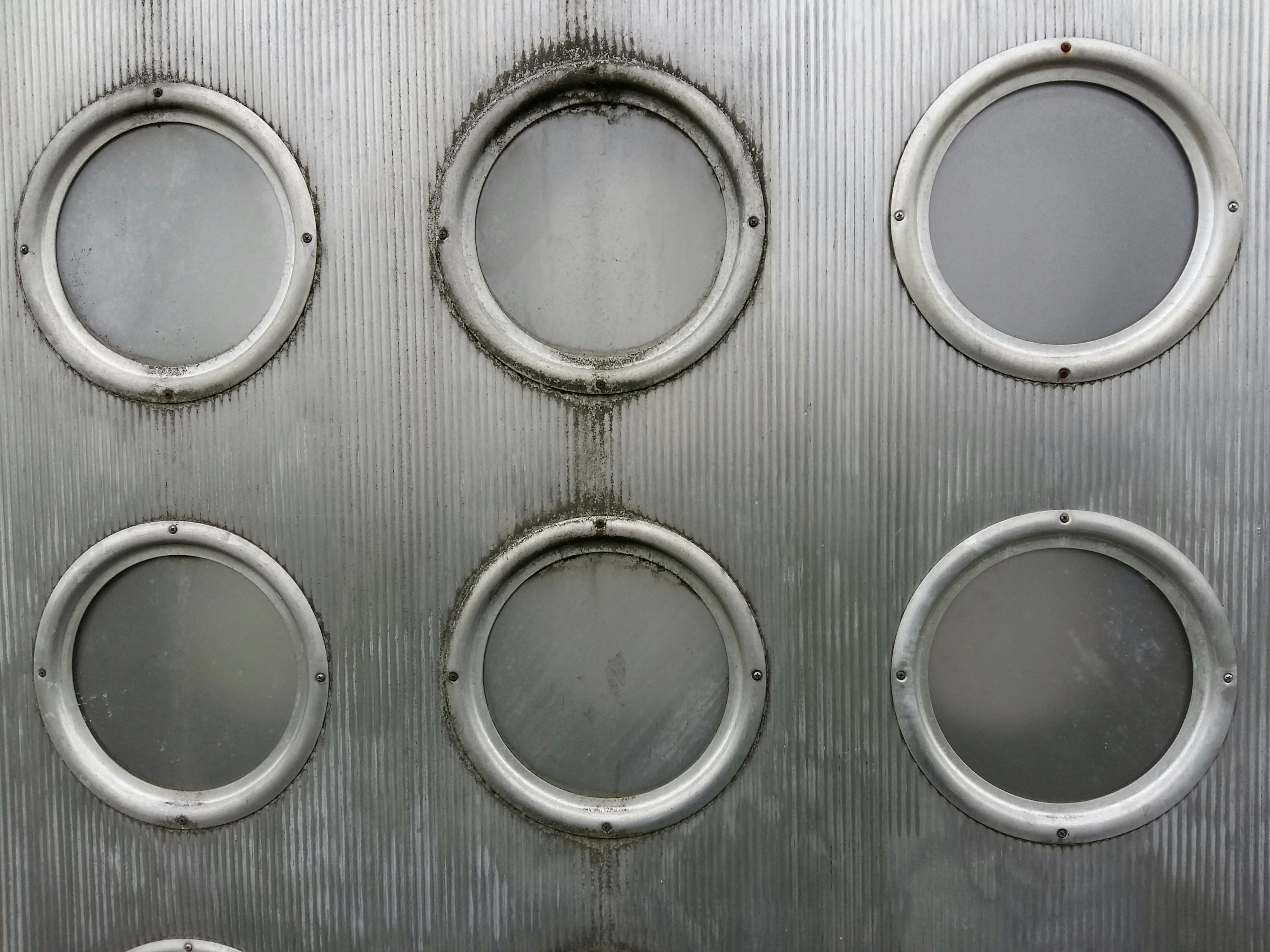 Six circular windows embedded in a textured metallic surface, showcasing a blend of transparency and reflections.