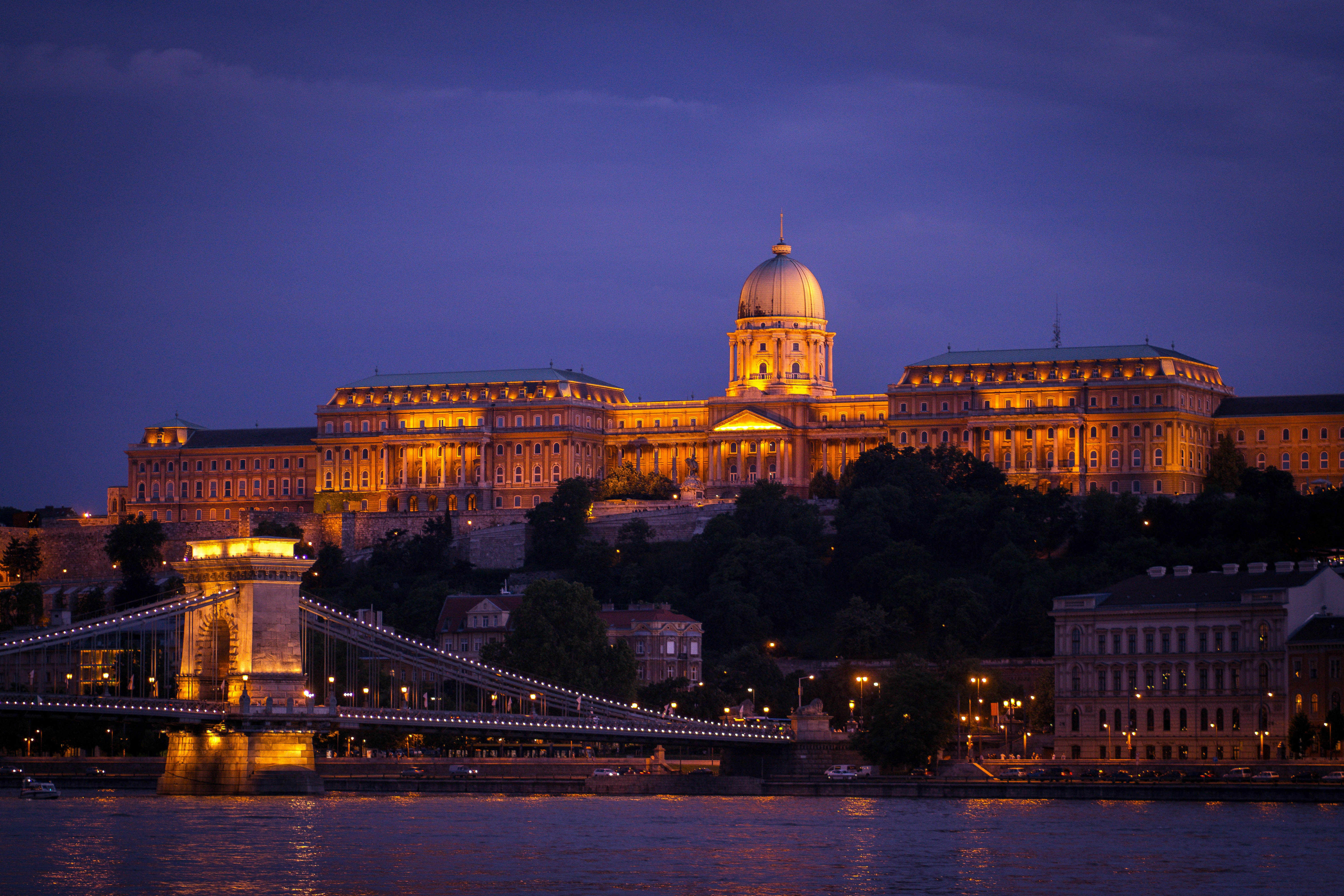 Historical castle aglow under a twilight sky, with a bridge spanning the river in the foreground.