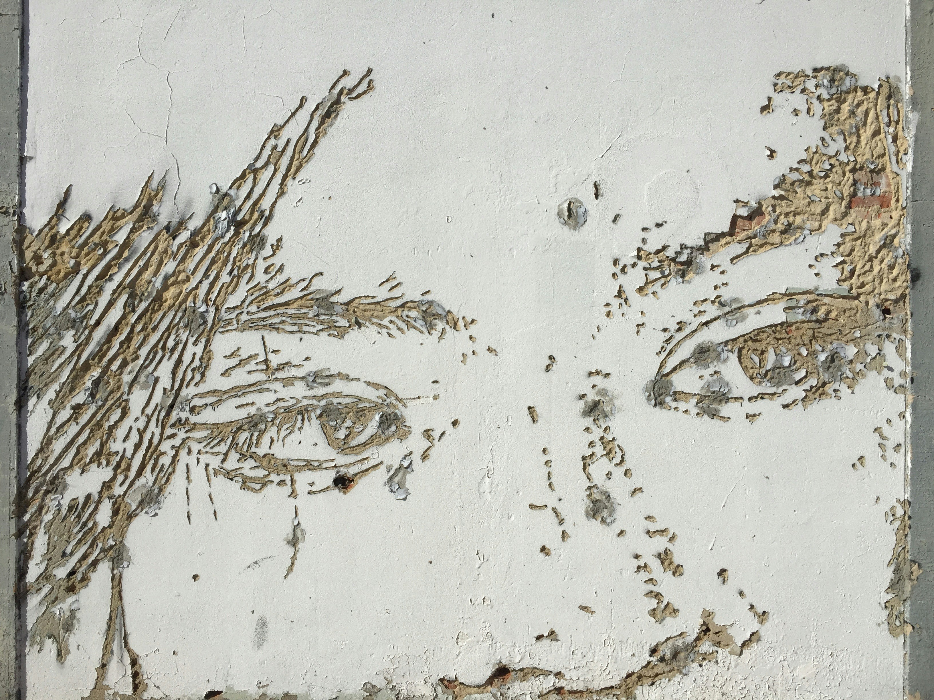 Abstract face etched into a worn concrete wall, showcasing distressed textures and earthy tones.