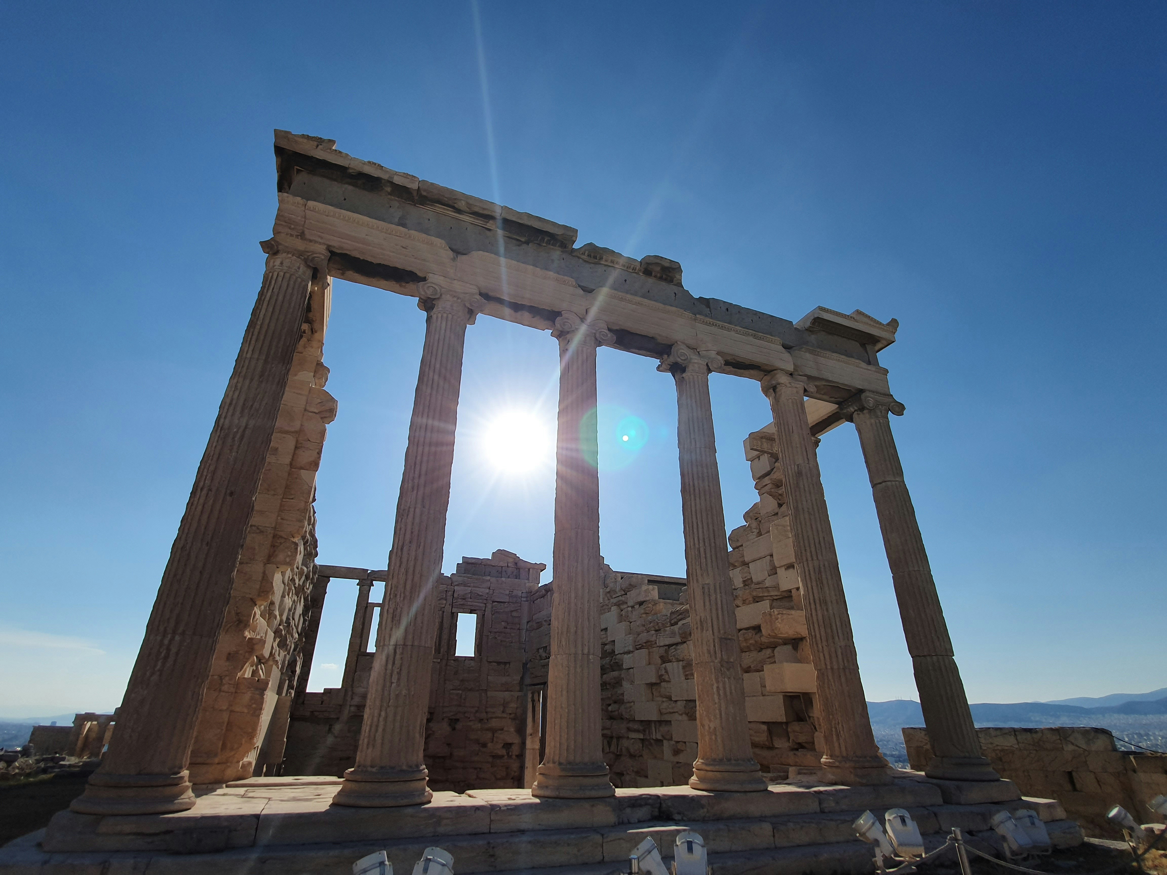 The Parthenon stands majestically against a clear blue sky, with sunlight streaming through its iconic columns, highlighting its ancient architecture.