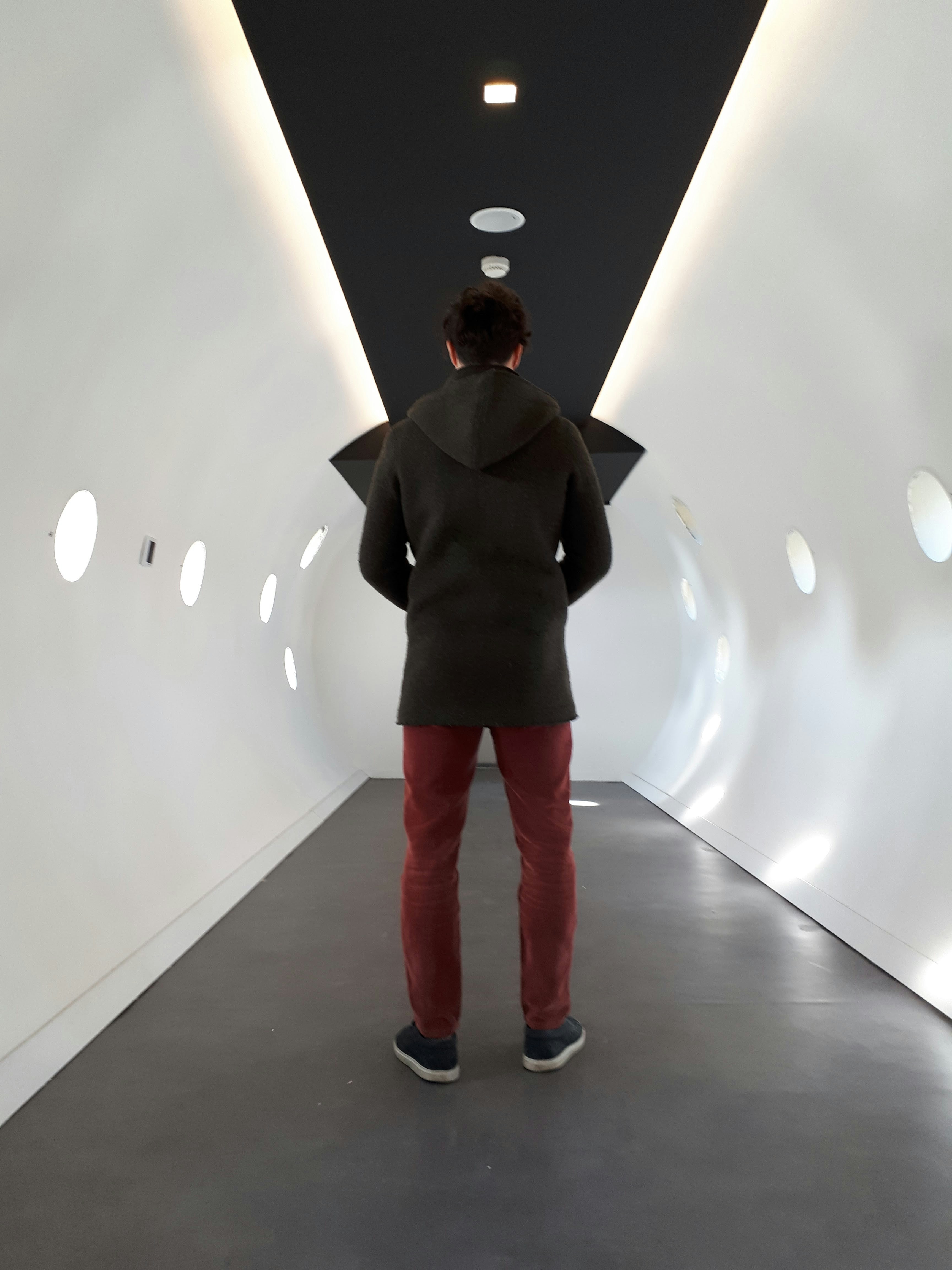 Traveler in the White Tunnel: Backward Stance Amid Circular Windows