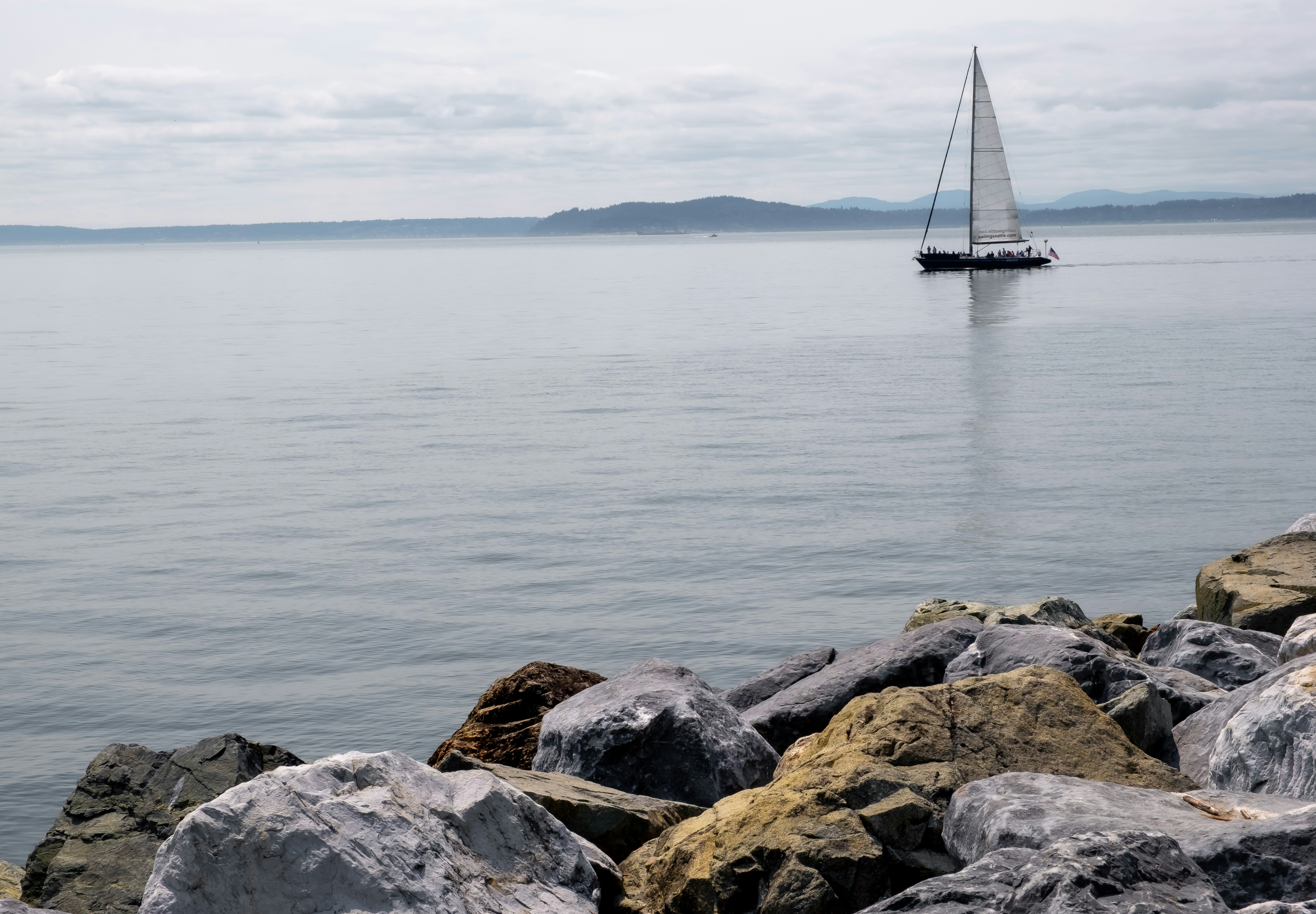 Glassy Sea, Granite Edge: A Sailboat on Quiet Tides
