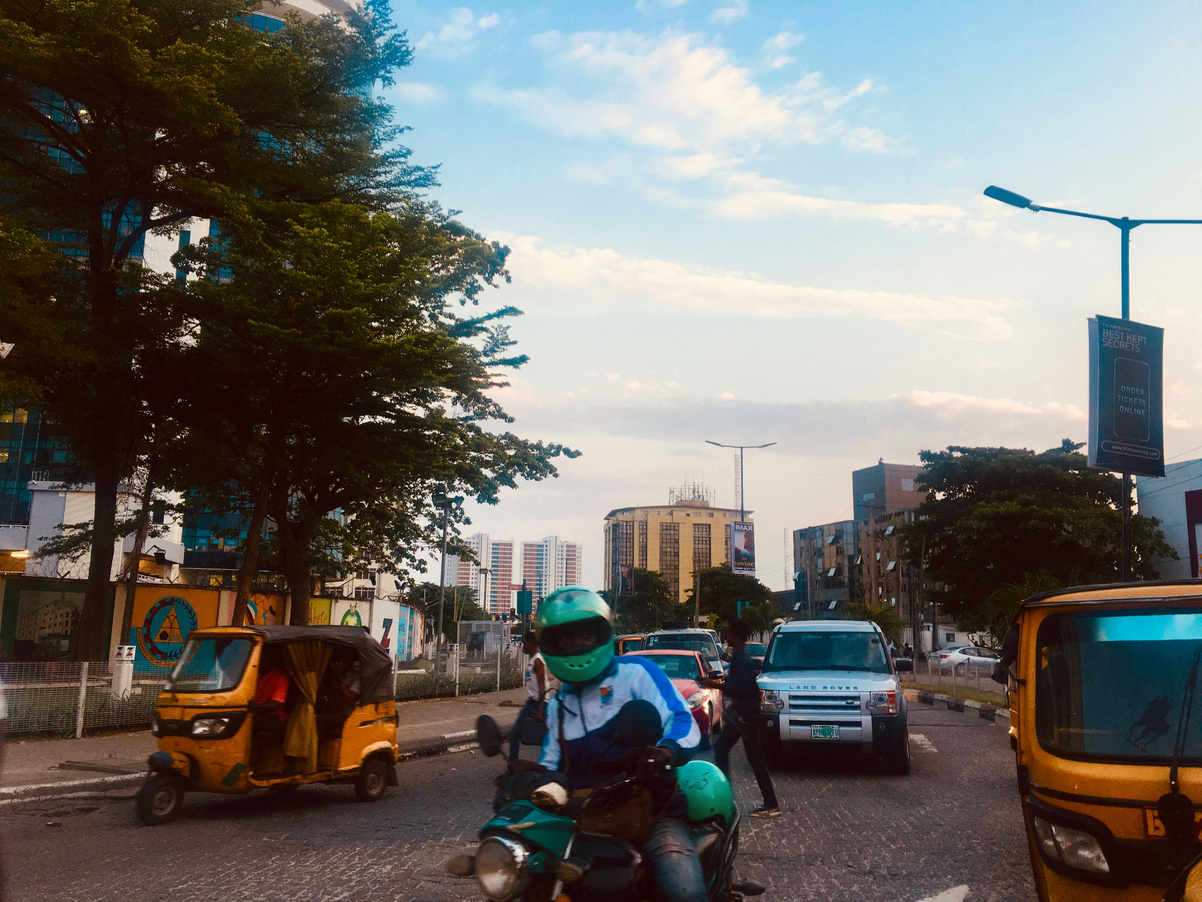 Busy city street with motorcycles, cars, and yellow rickshaws under a blue sky.