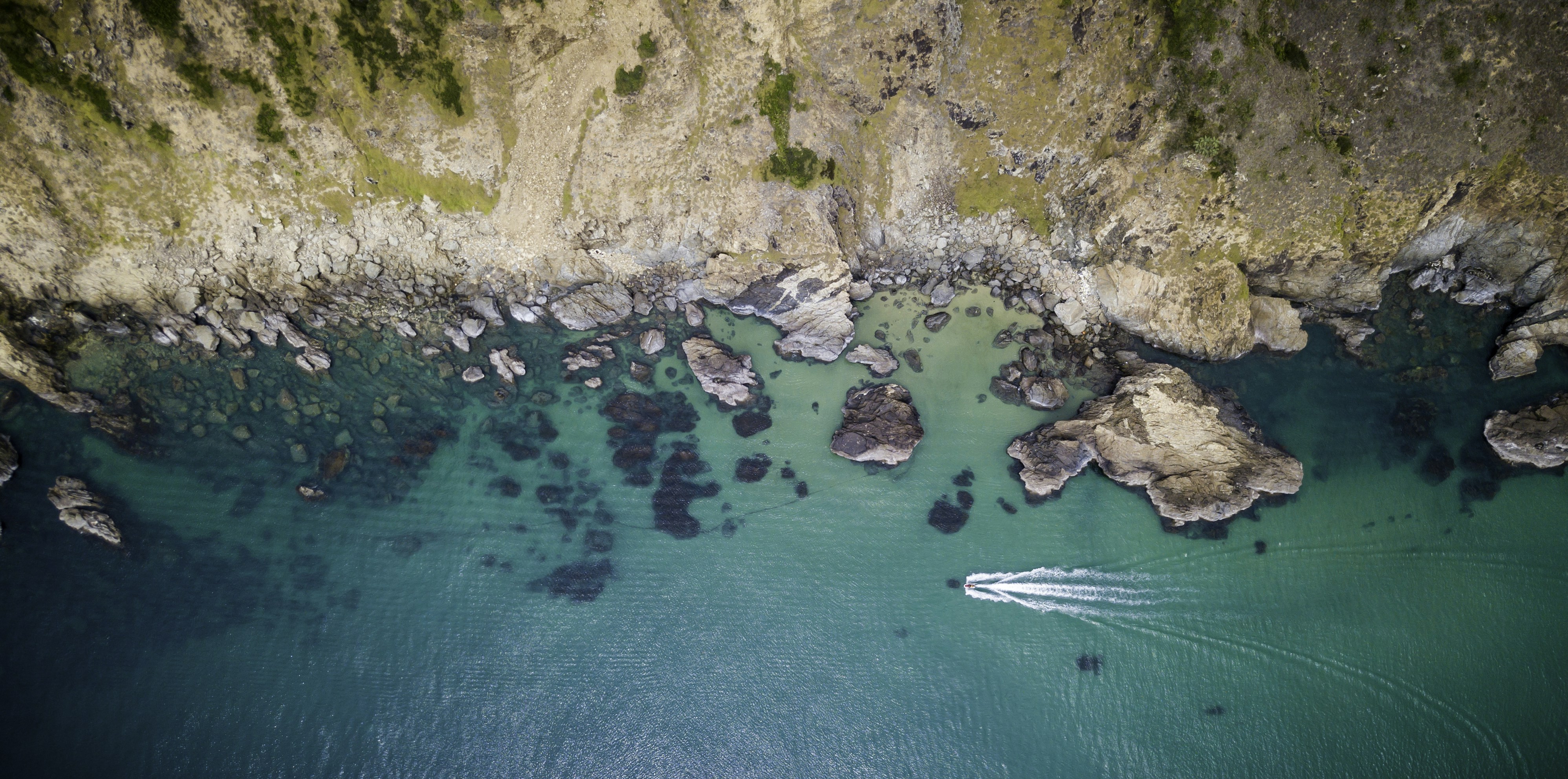 Aerial view of a boat navigating clear turquoise waters near a rocky coastline.
