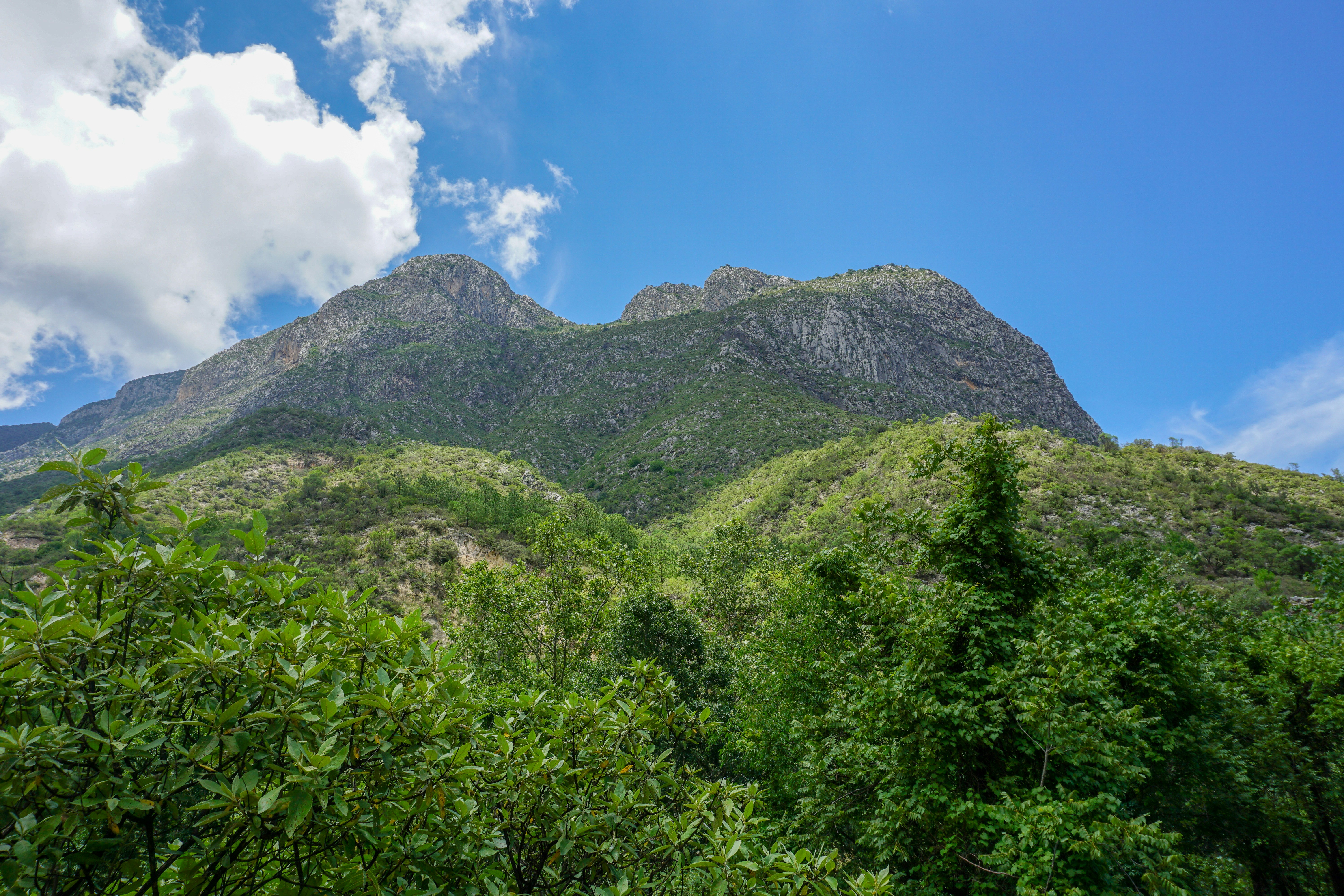 Lush green mountains beneath a bright blue sky with scattered clouds.
