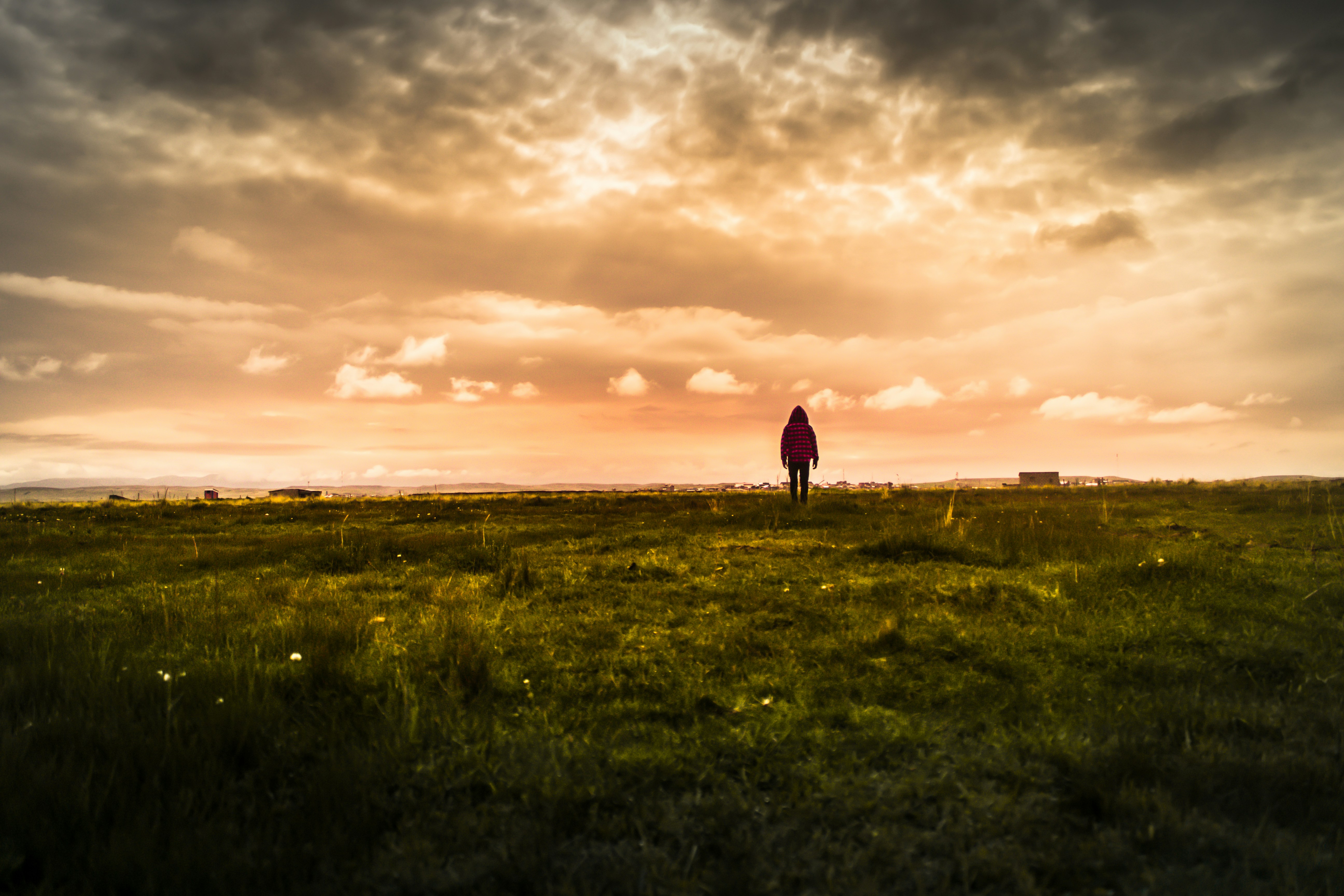 Person walking on a grassy field beneath a dramatic, orange-tinged sky at sunset.