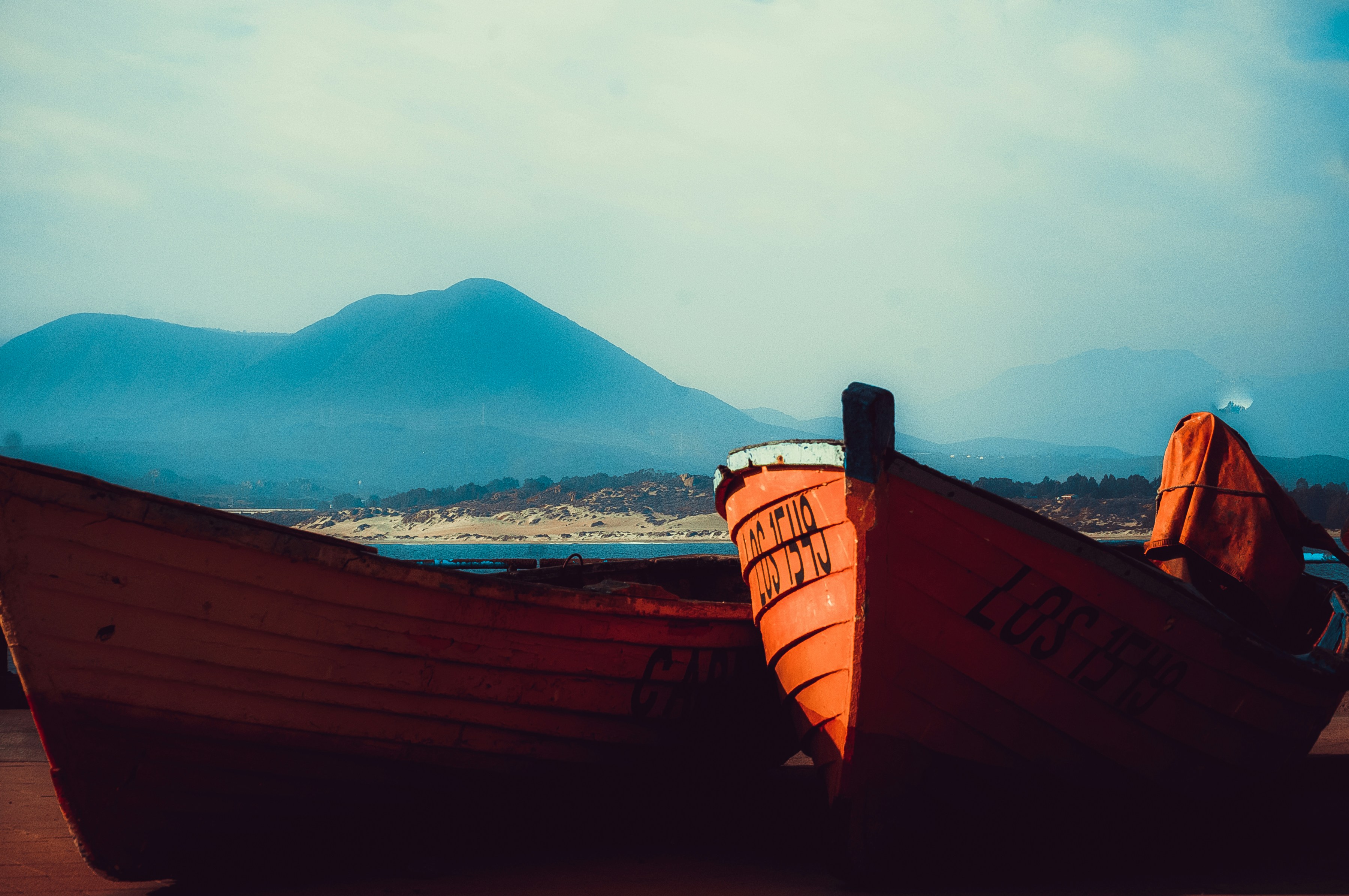 Red Boats at Dusk: Quiet Coastline and Distant Mountains