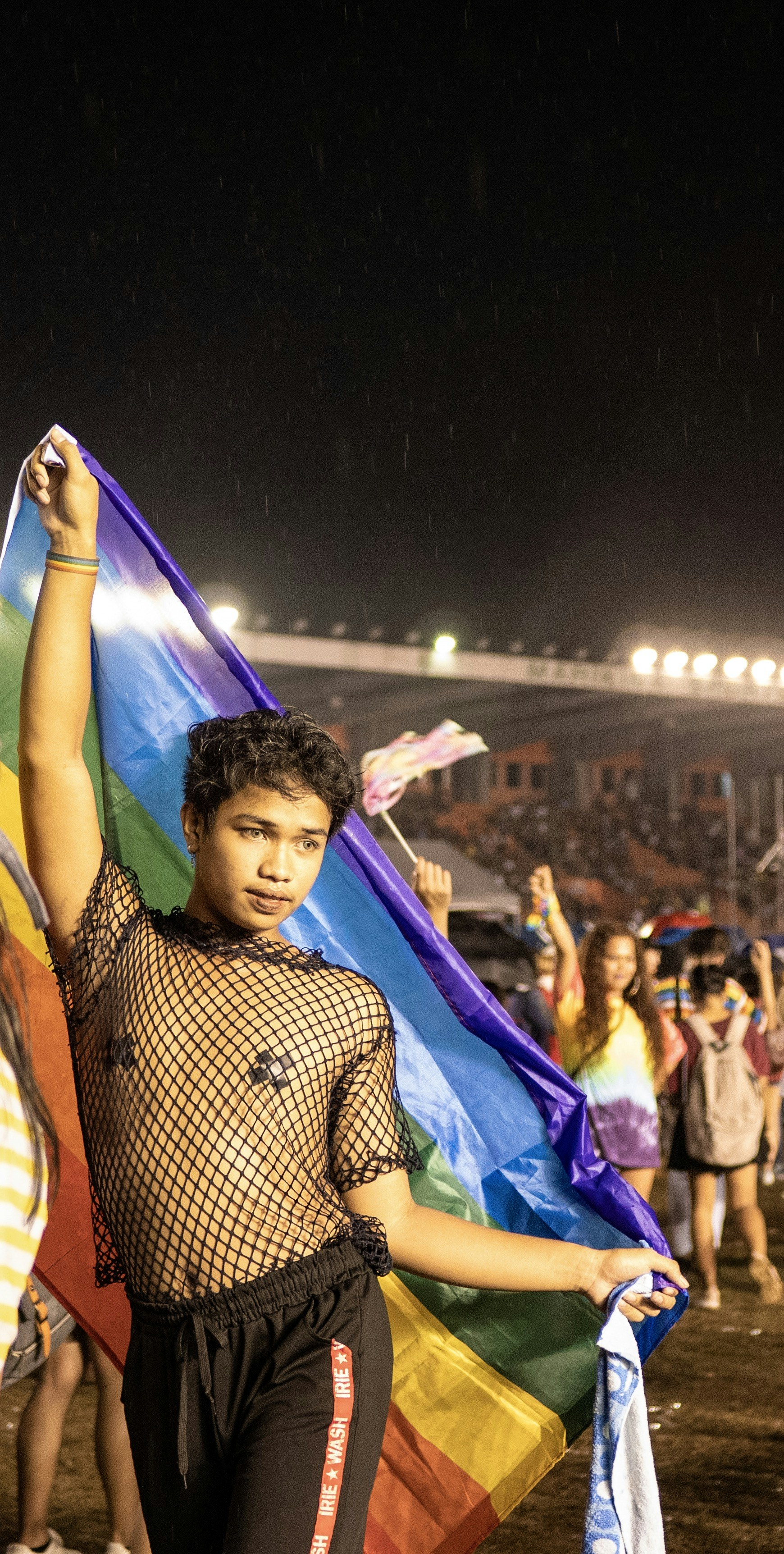 Pride Parade: A fearless dancer draped in a rainbow flag under night lights