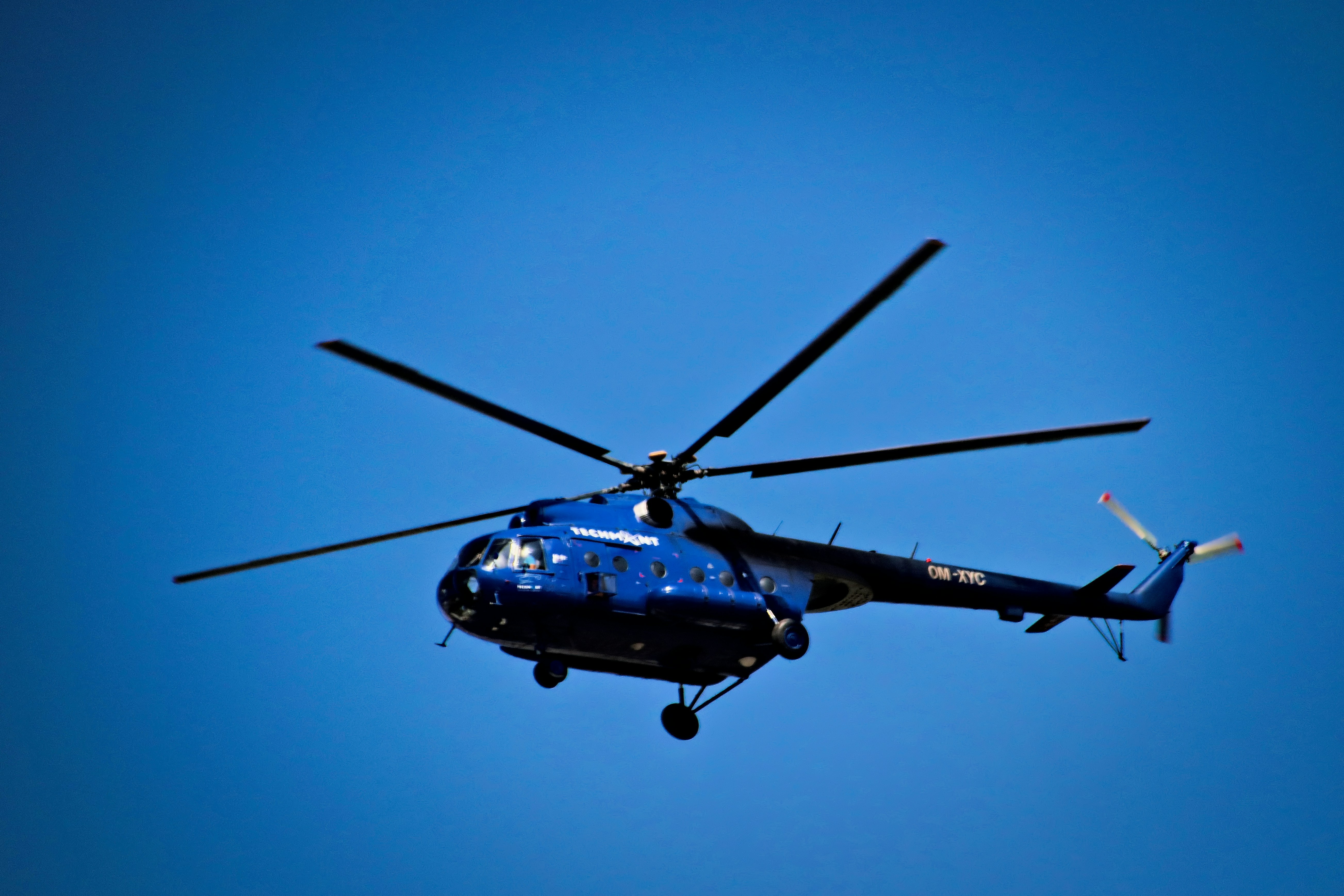 Blue helicopter flying against a clear blue sky, showcasing its dynamic rotor blades and sleek design.