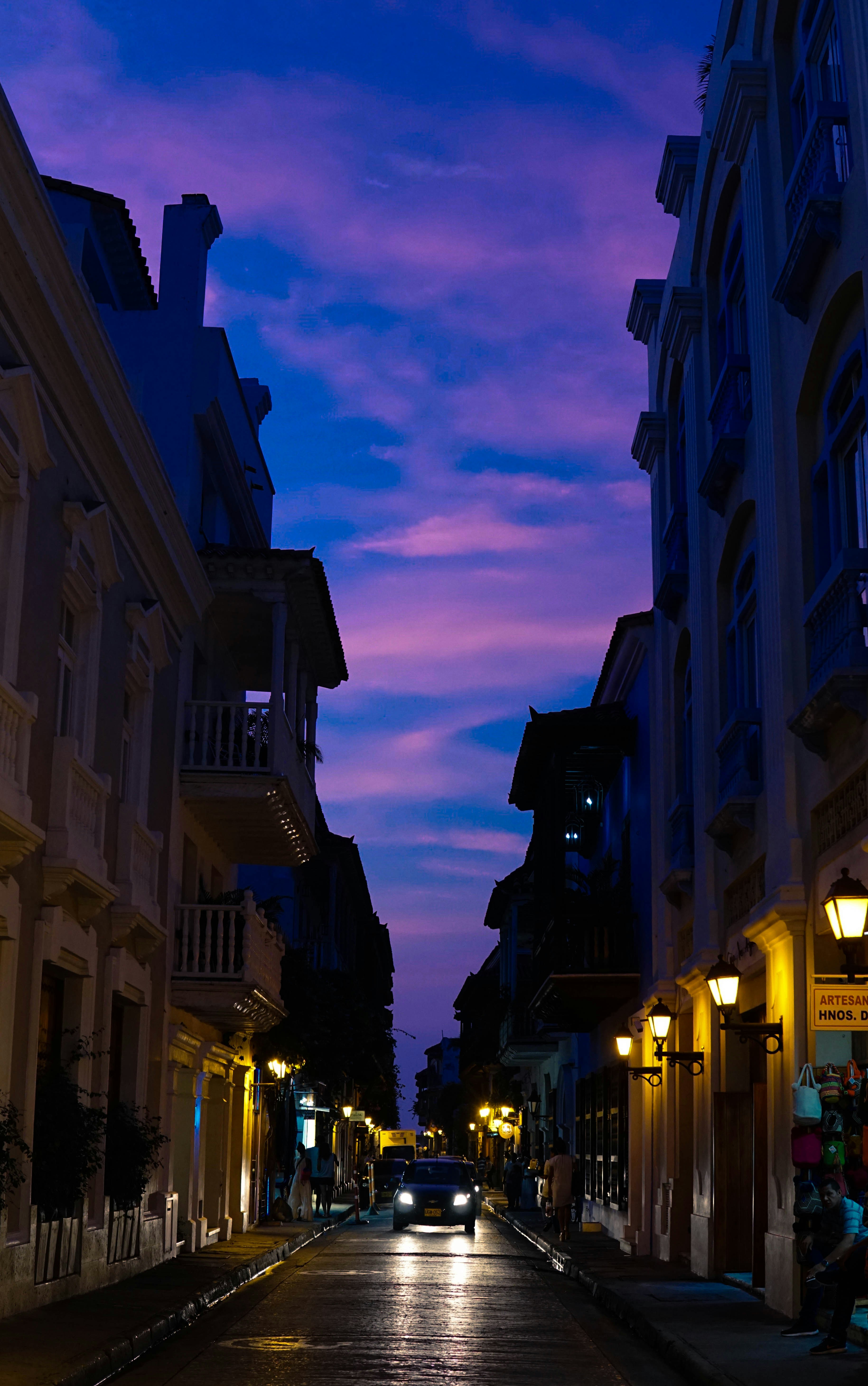 Narrow street framed by historic buildings under a vibrant purple and blue twilight sky.