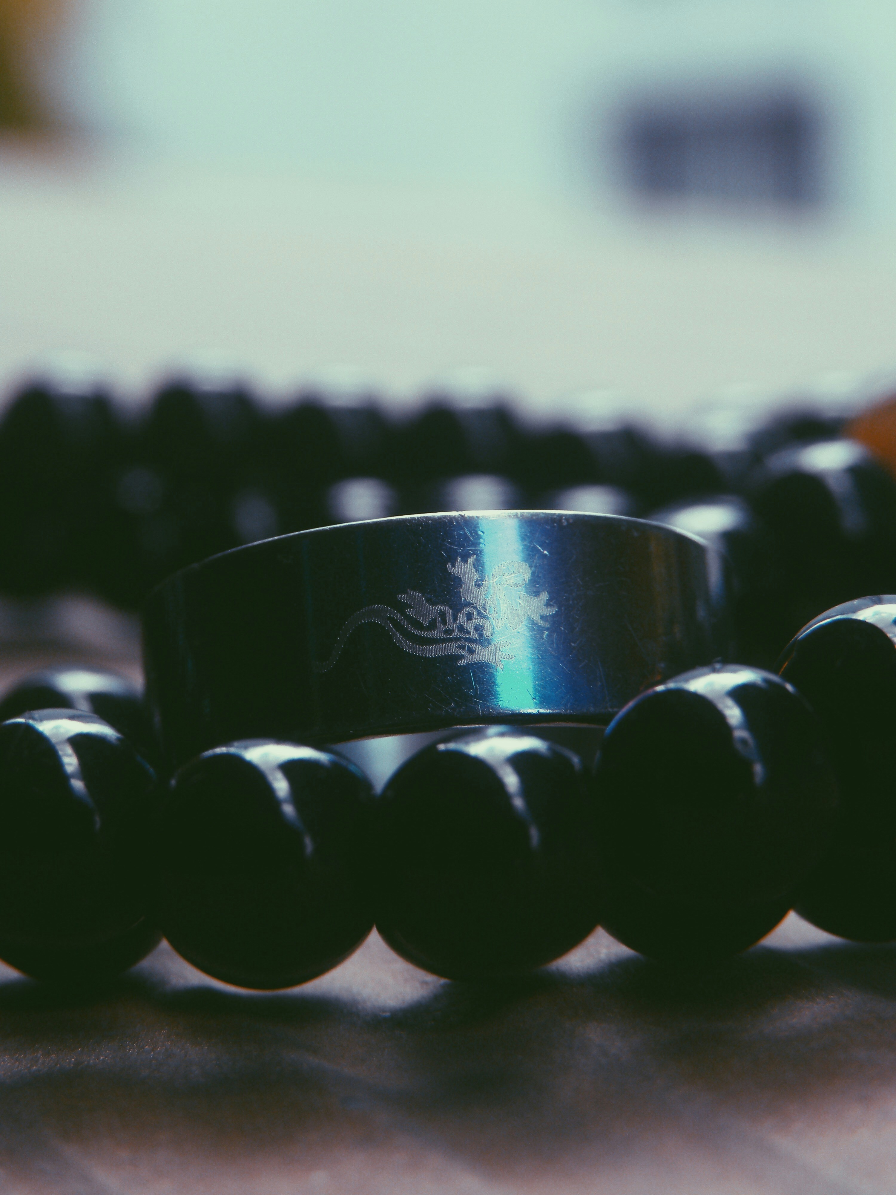A polished silver ring with intricate dragon engraving rests atop a strand of glossy black beads, showcasing a harmonious blend of materials.