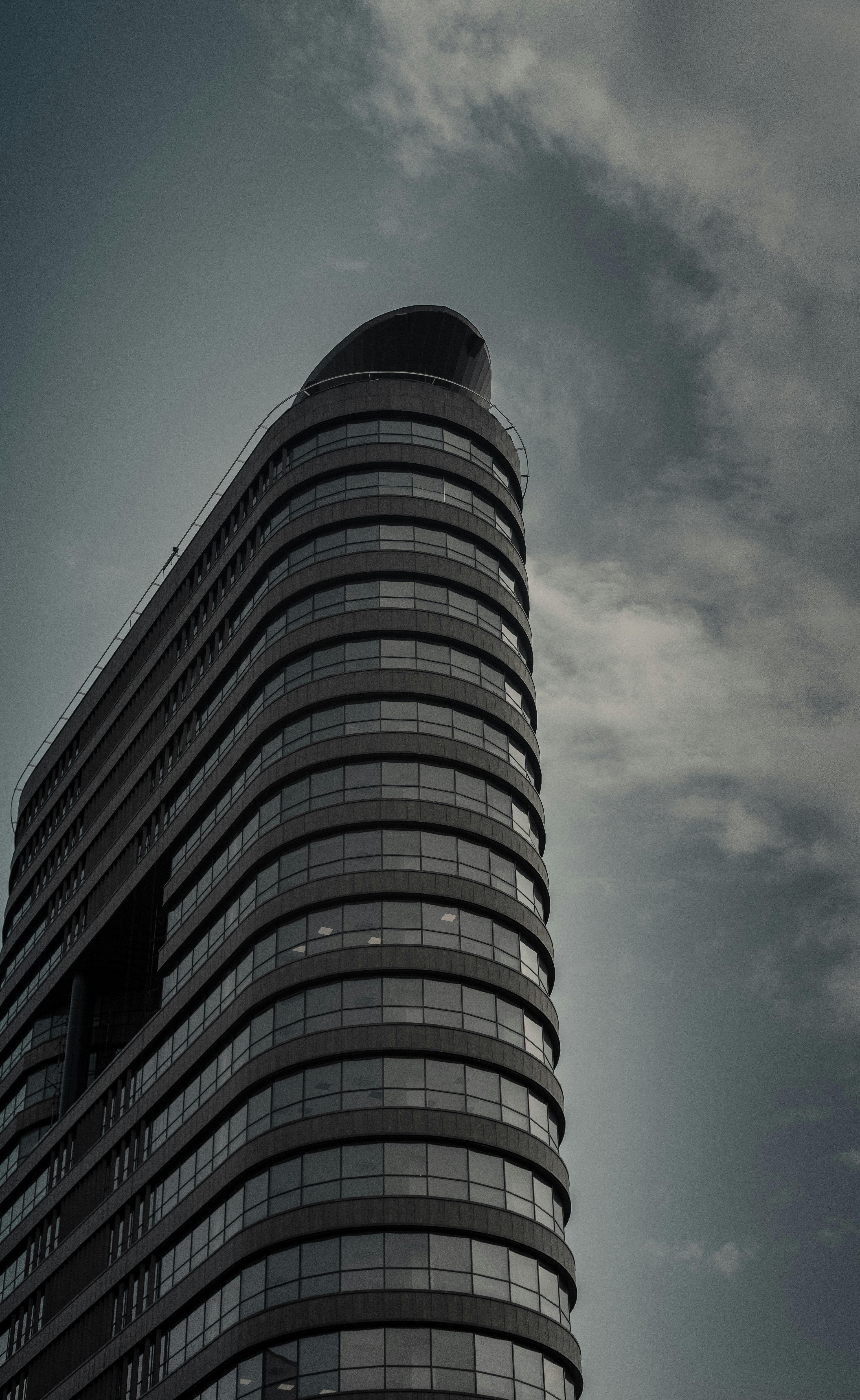 Sleek, curved skyscraper reaching into the cloudy sky, showcasing contemporary architectural design.