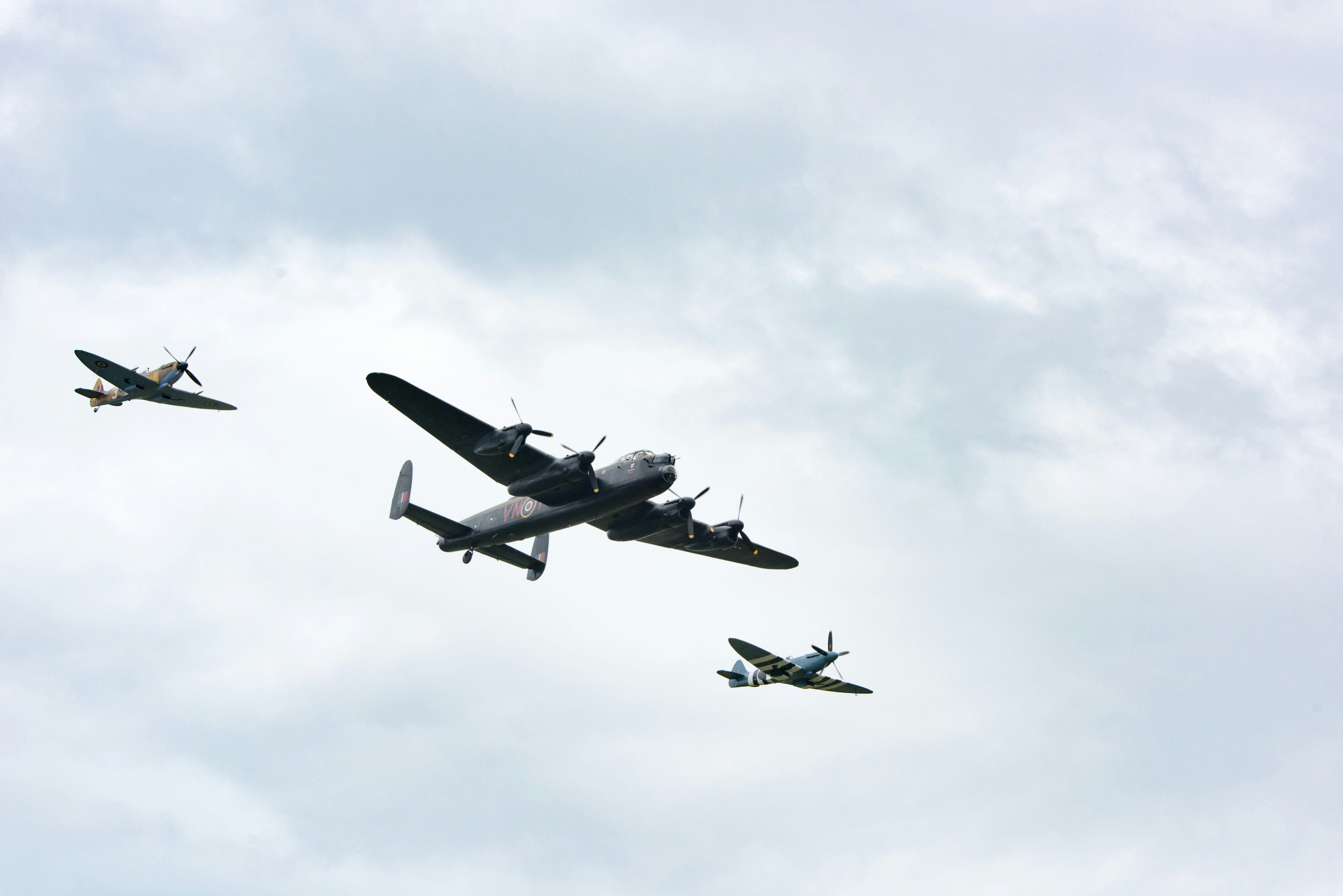 Historic aircraft flying in formation against a cloudy sky, showcasing their iconic designs and rich aviation history.
