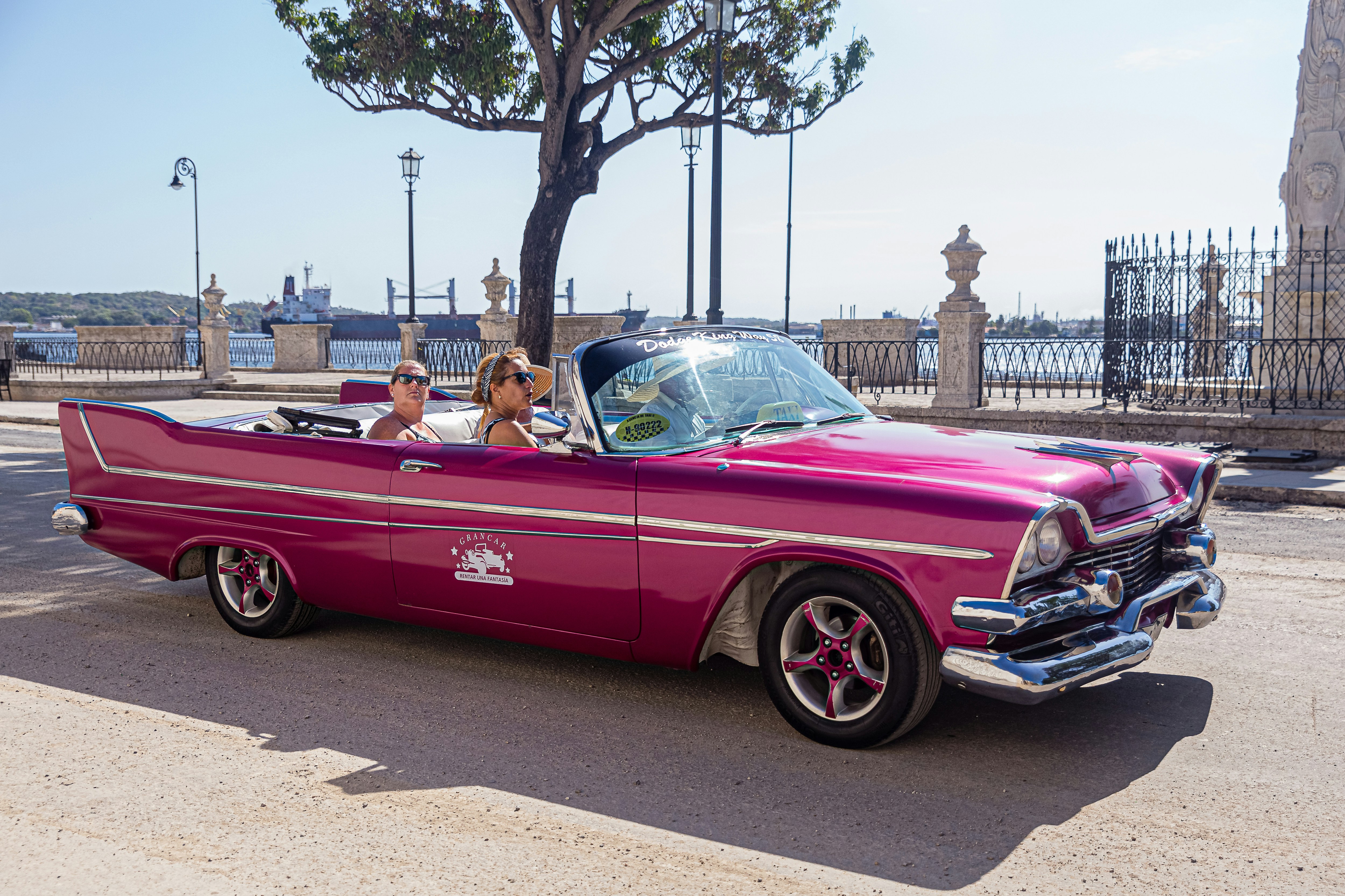 Vintage pink convertible cruising along a sunny seaside promenade.