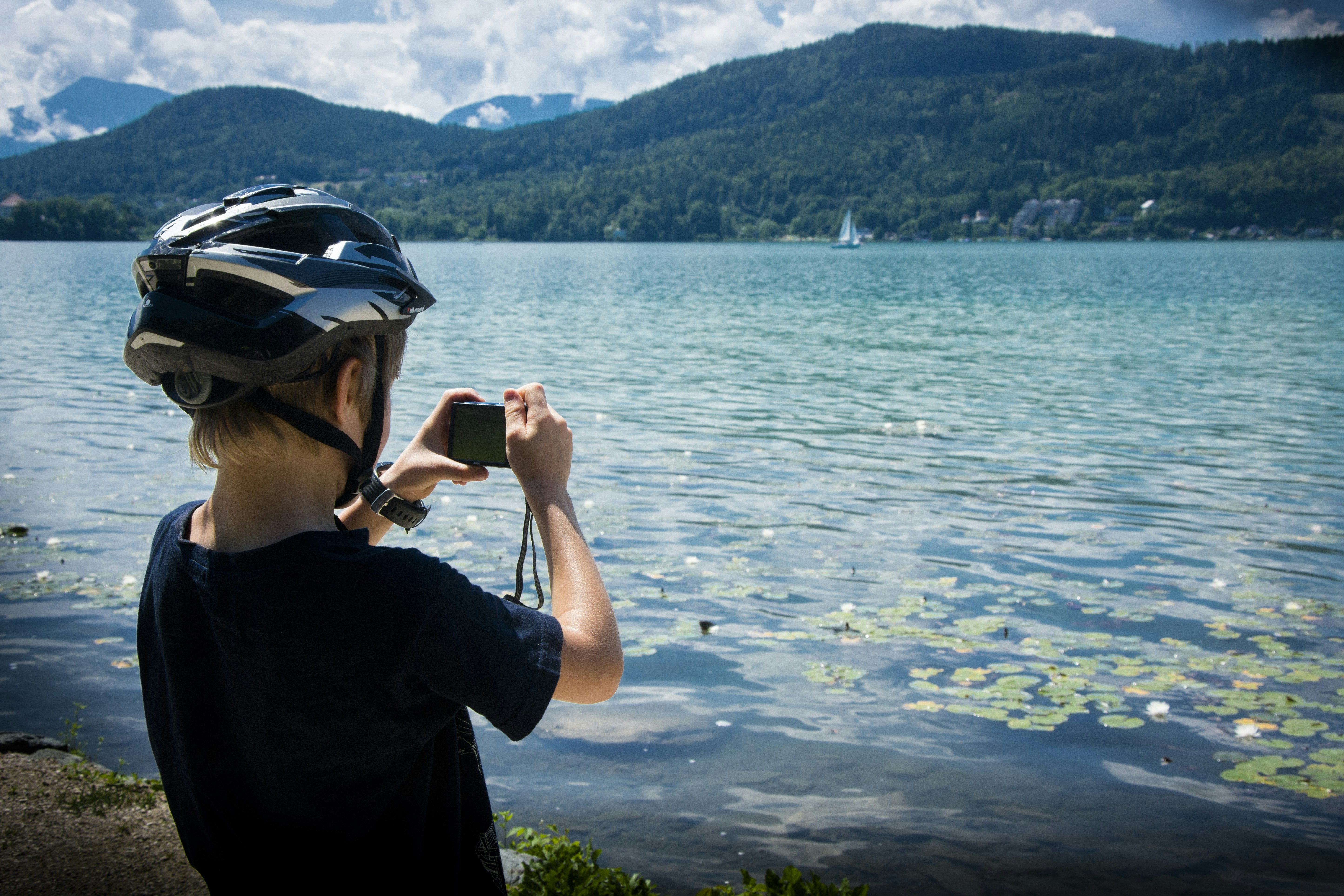 Helmeted Photographer at the Lakefront Framing Alpine Calm with a Smartphone