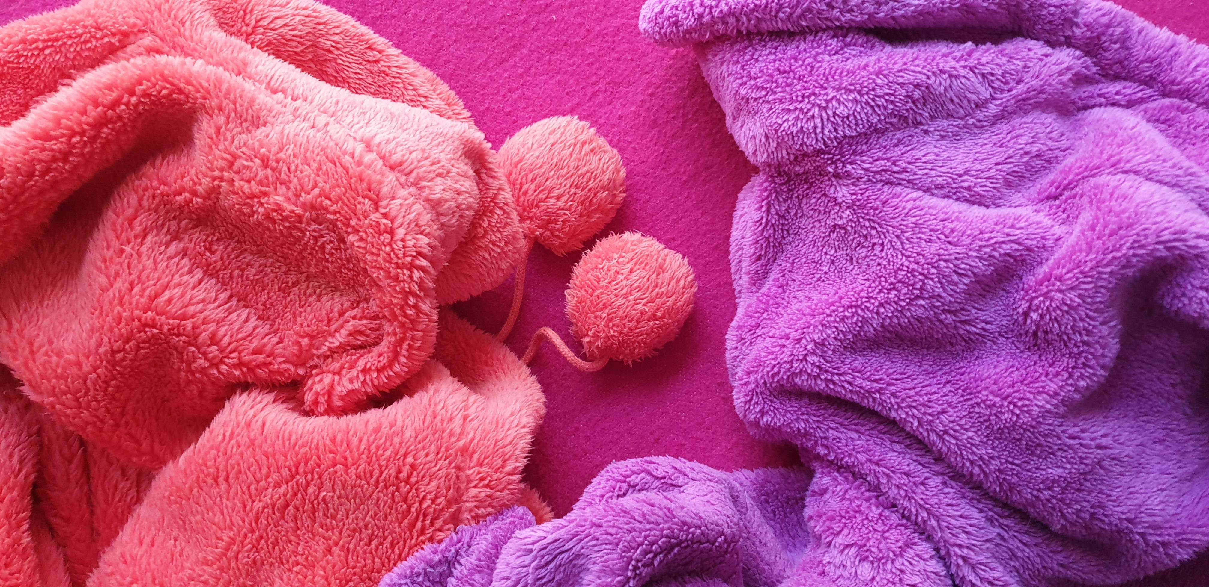 Two soft, plush blankets in vibrant pink and purple hues, intertwined on a matching background, creating a cozy and inviting atmosphere.