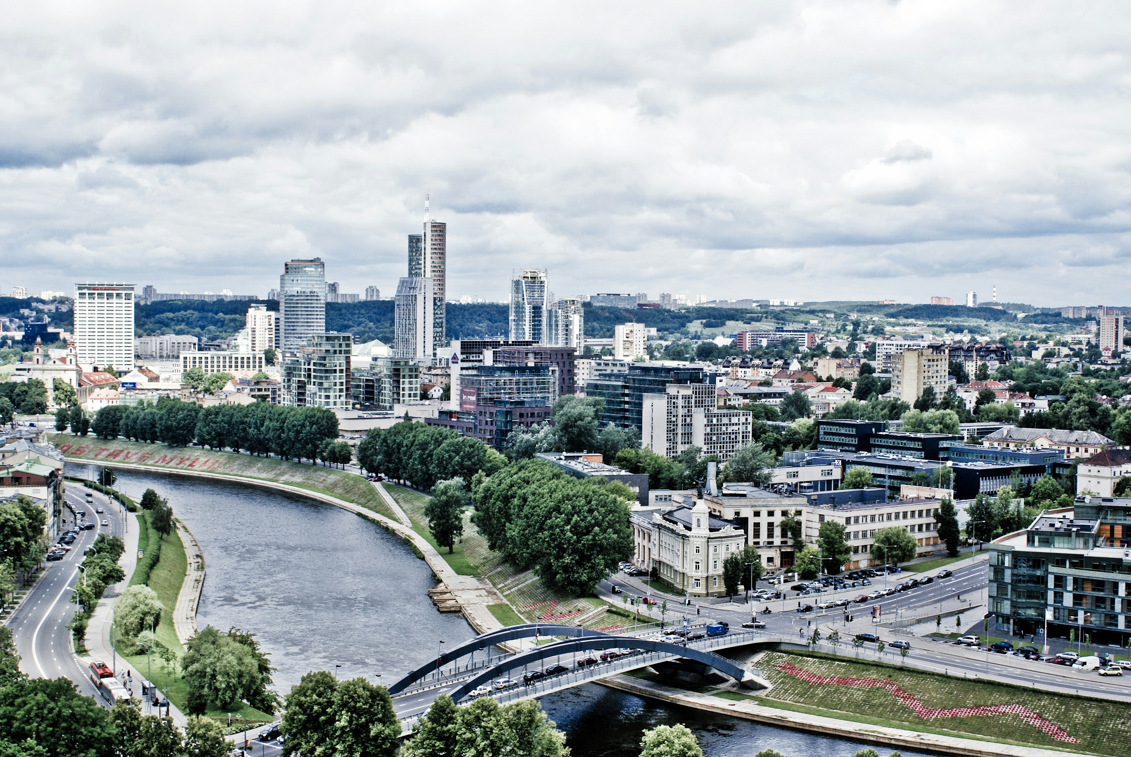 A panoramic view of a bustling city skyline with a river winding through green landscapes, showcasing modern architecture and urban life.