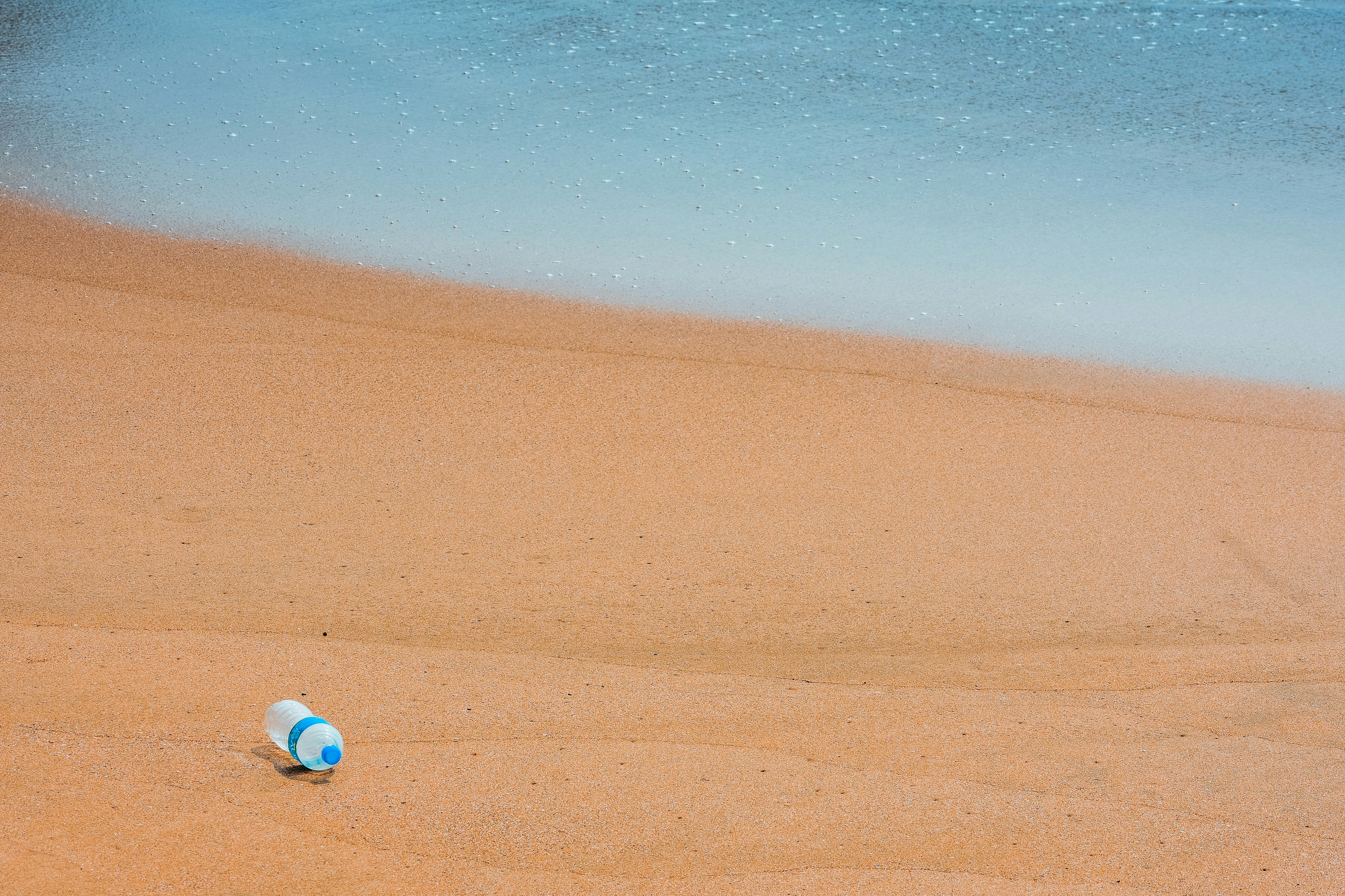 Blue-White Bottle Cap at the Edge of Sand and Sea