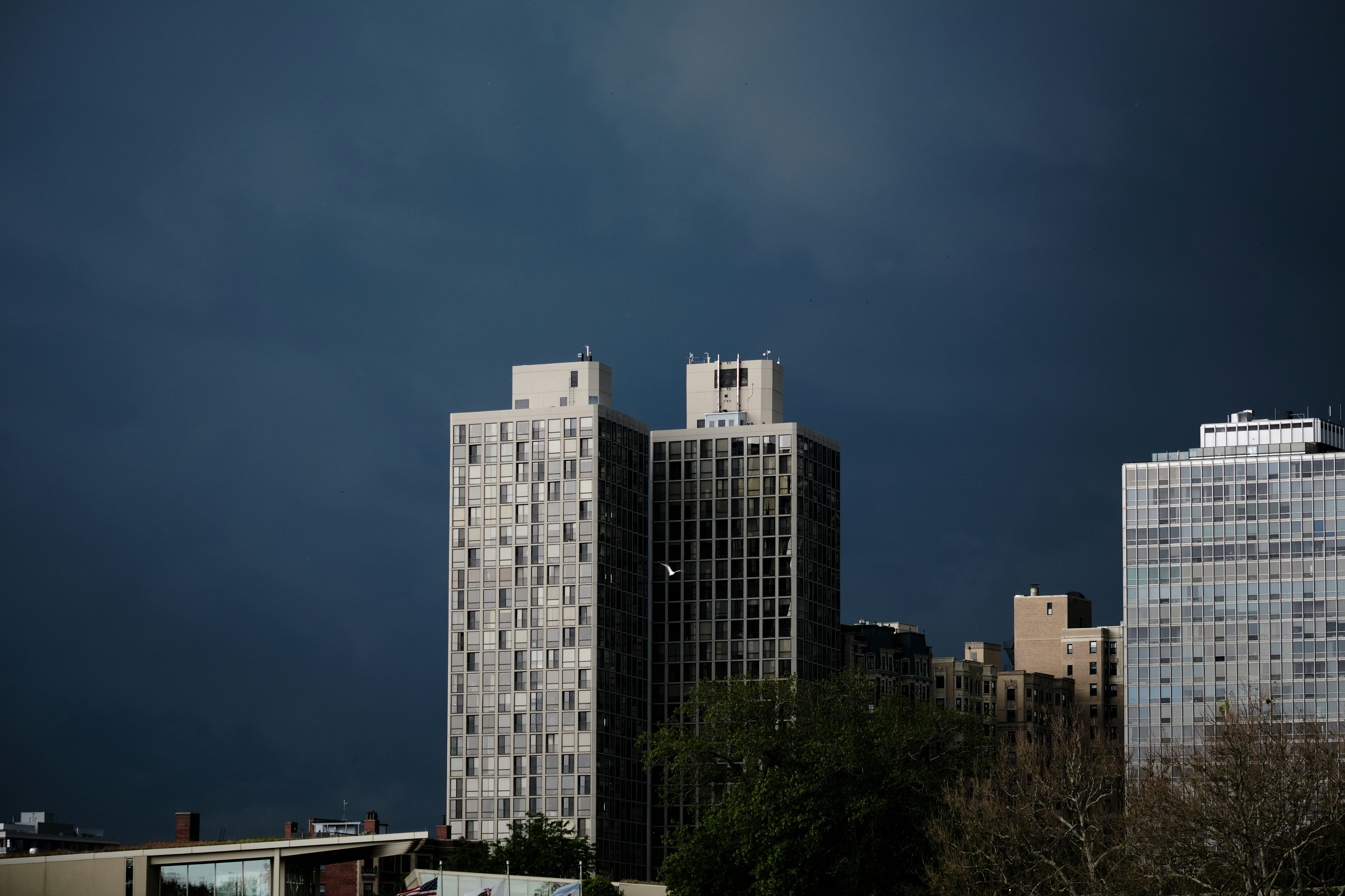 Two modern high-rise buildings stand against a dark, stormy sky, hinting at an impending downpour.