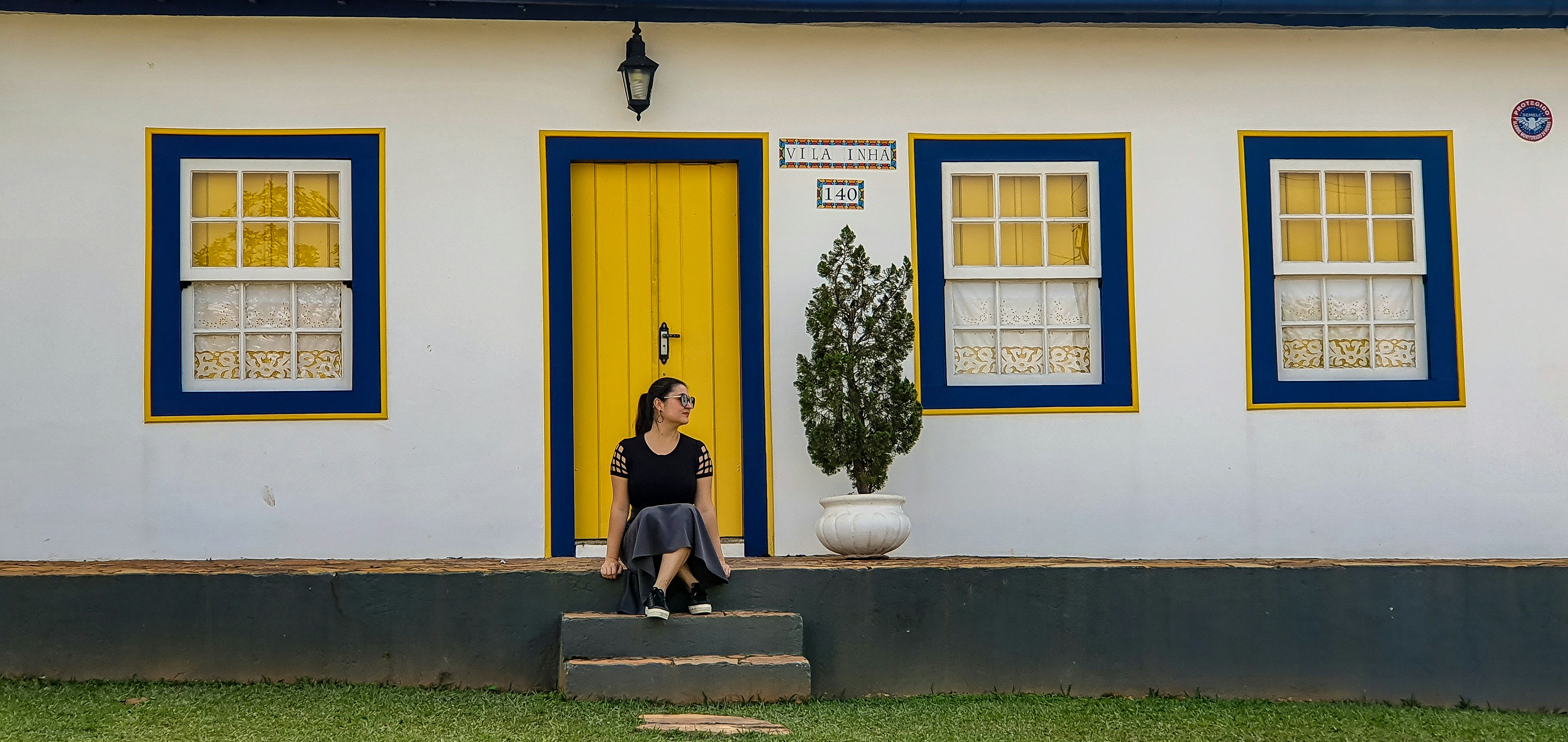 Woman sitting on steps in front of a house with a bright yellow door and blue-trimmed windows.