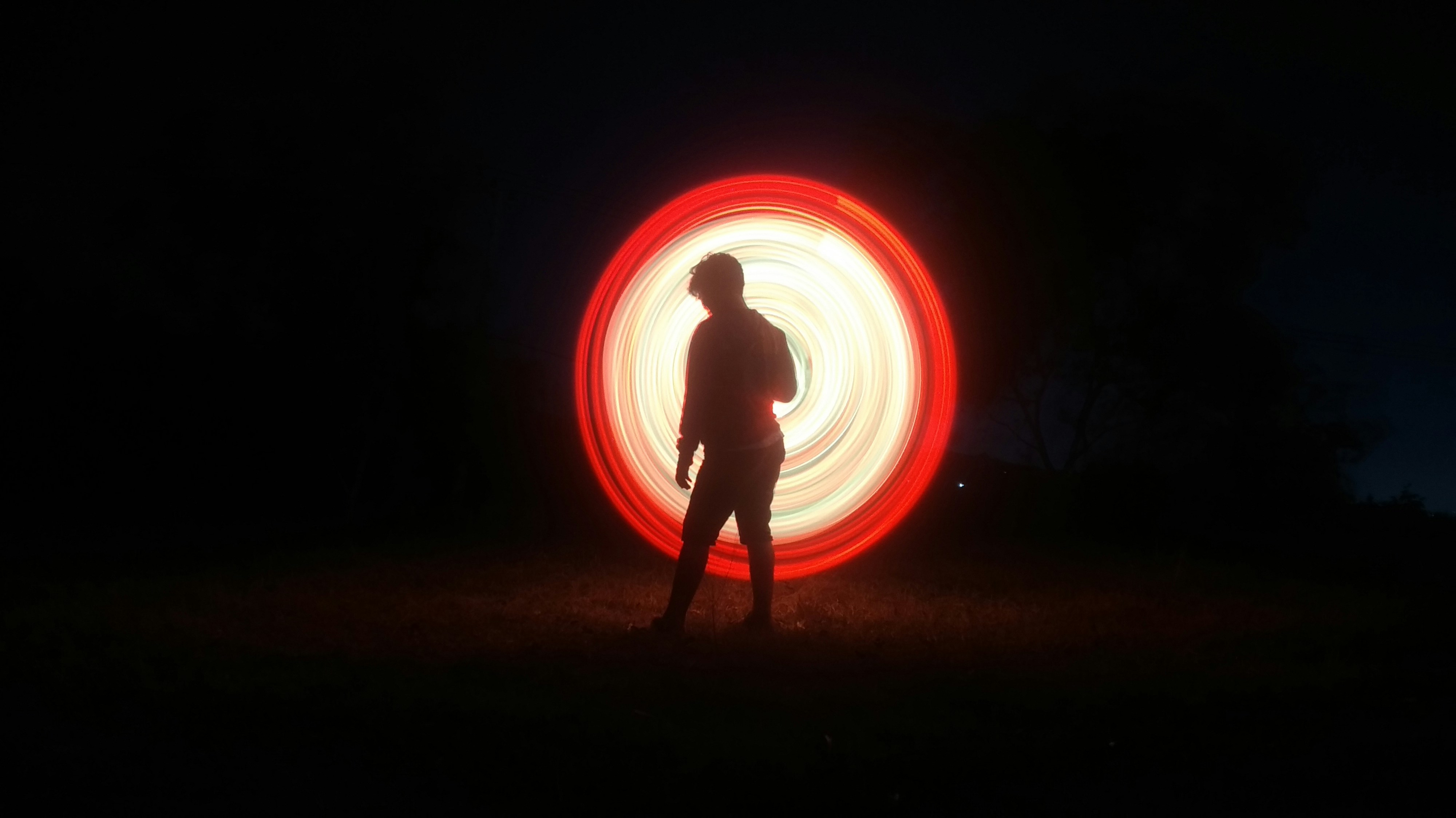 Silhouette of a person framed by a swirling red and white light circle against a dark background.