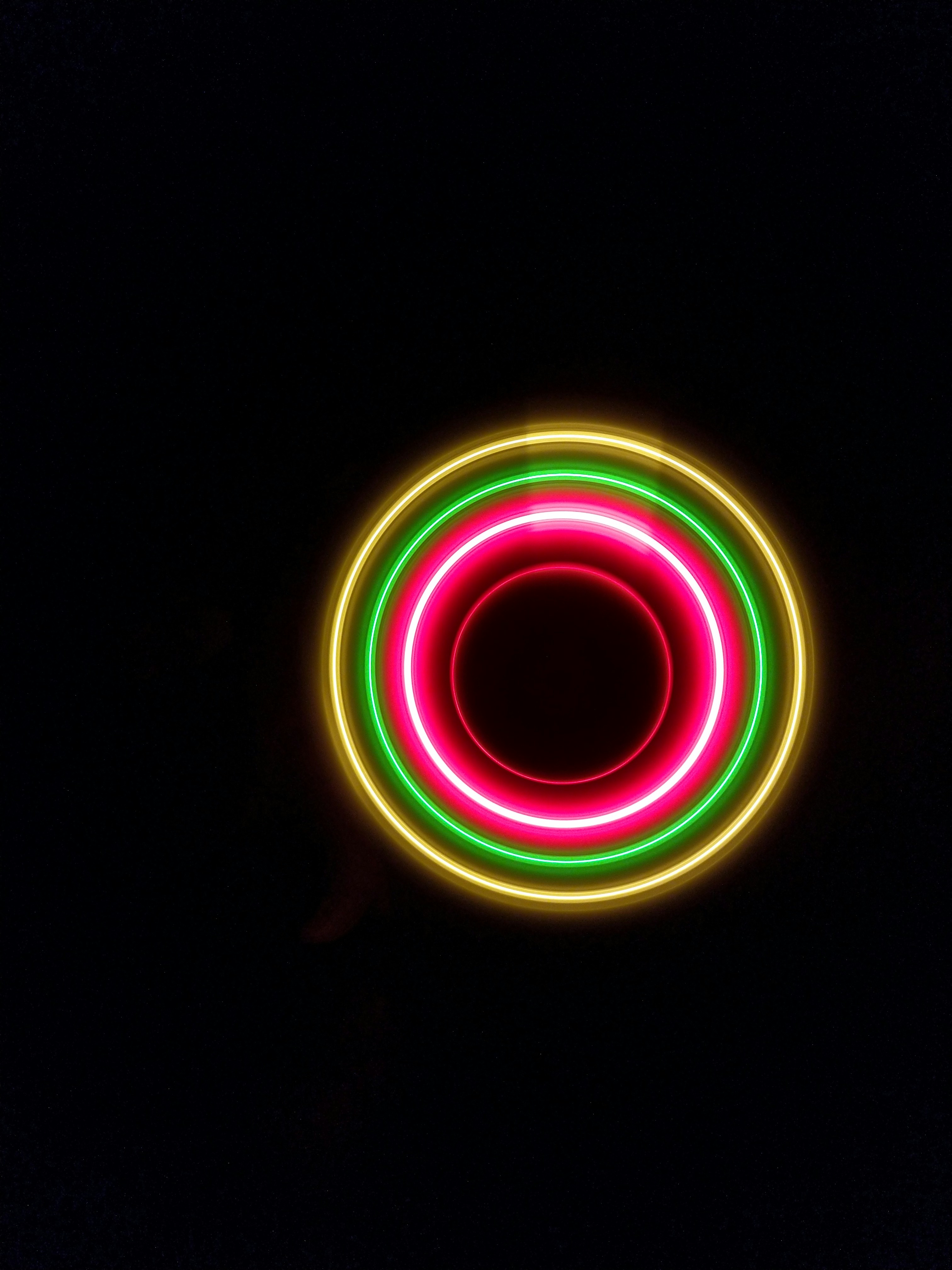 Concentric circles of vibrant neon lights in pink, green, and yellow against a black background, creating a mesmerizing visual effect.