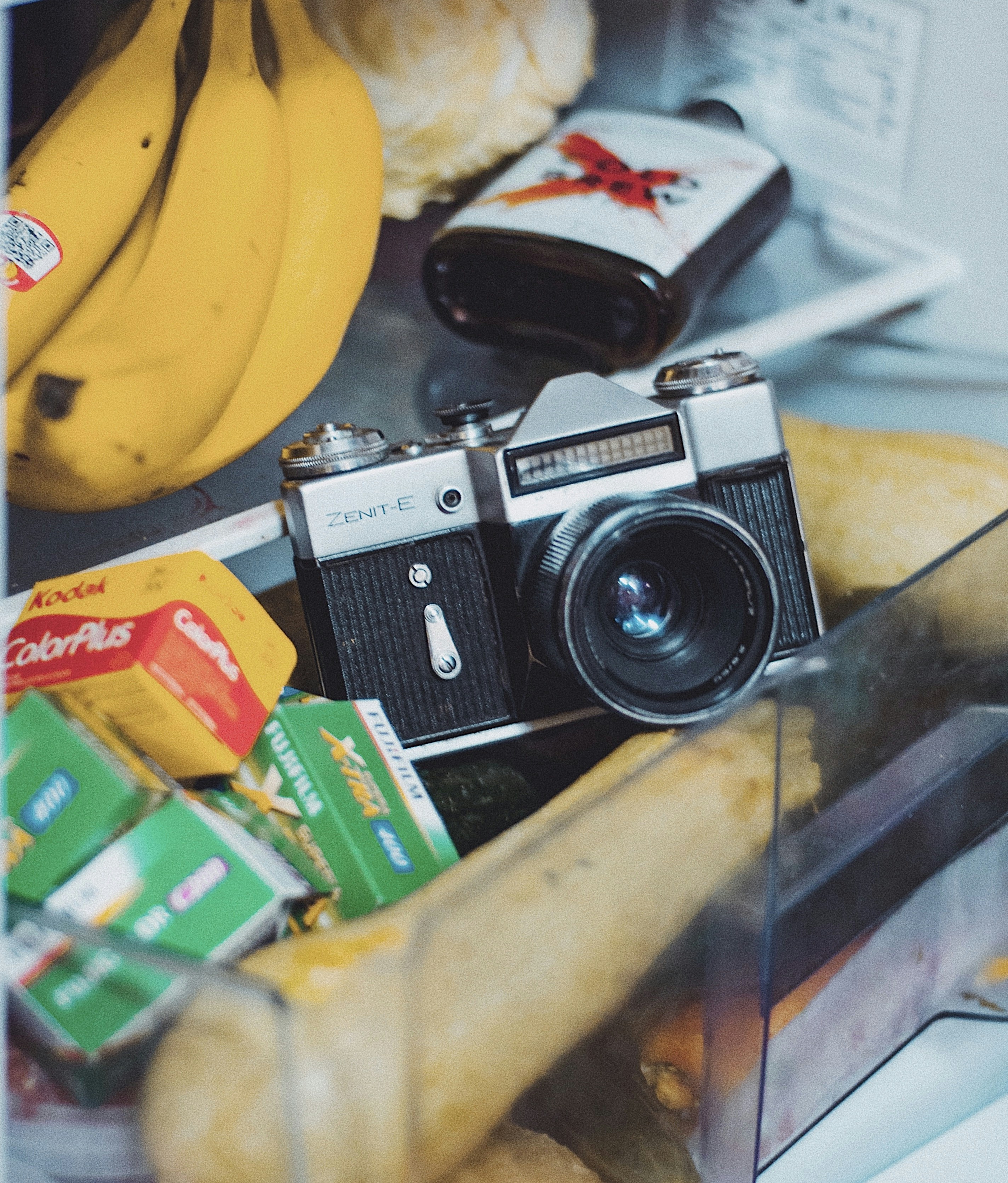 Zenit-E in a Glass Display Case: A Vintage Camera Surrounded by Bananas and Colorful Boxes