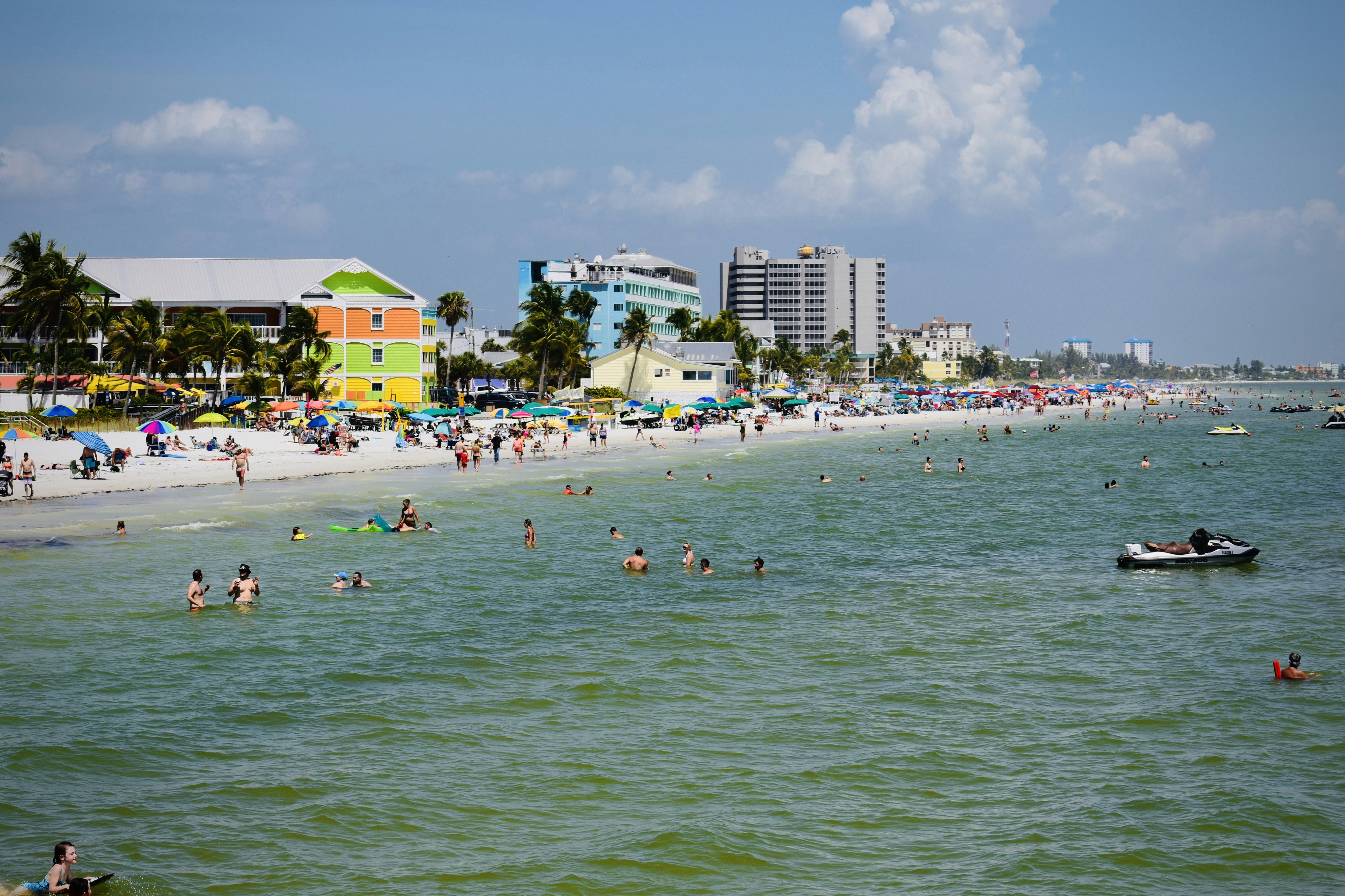 Vibrant beach scene filled with sunbathers and colorful umbrellas along the shoreline, with distant buildings adding to the coastal charm.