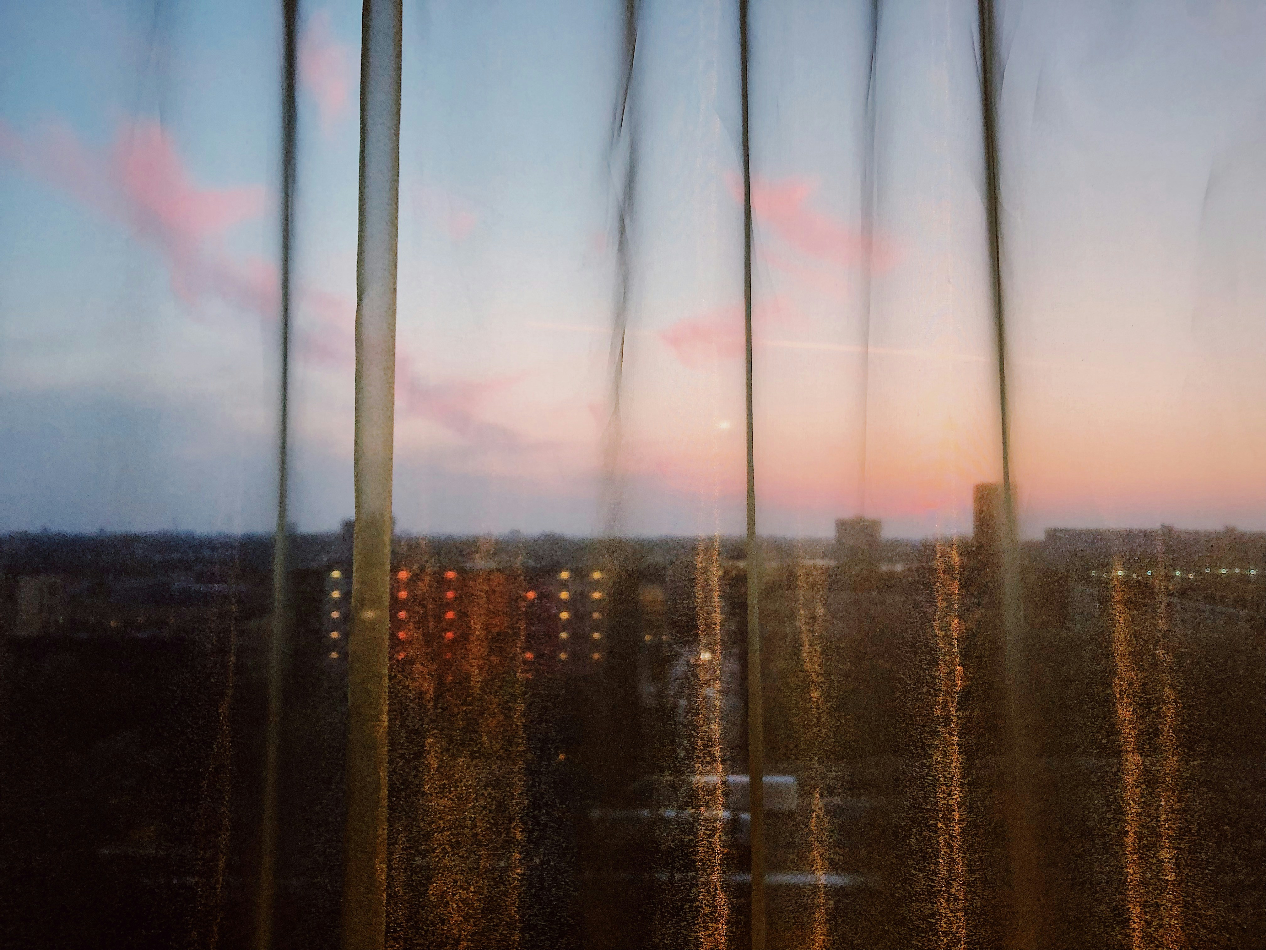 City skyline viewed through translucent curtains at sunset.