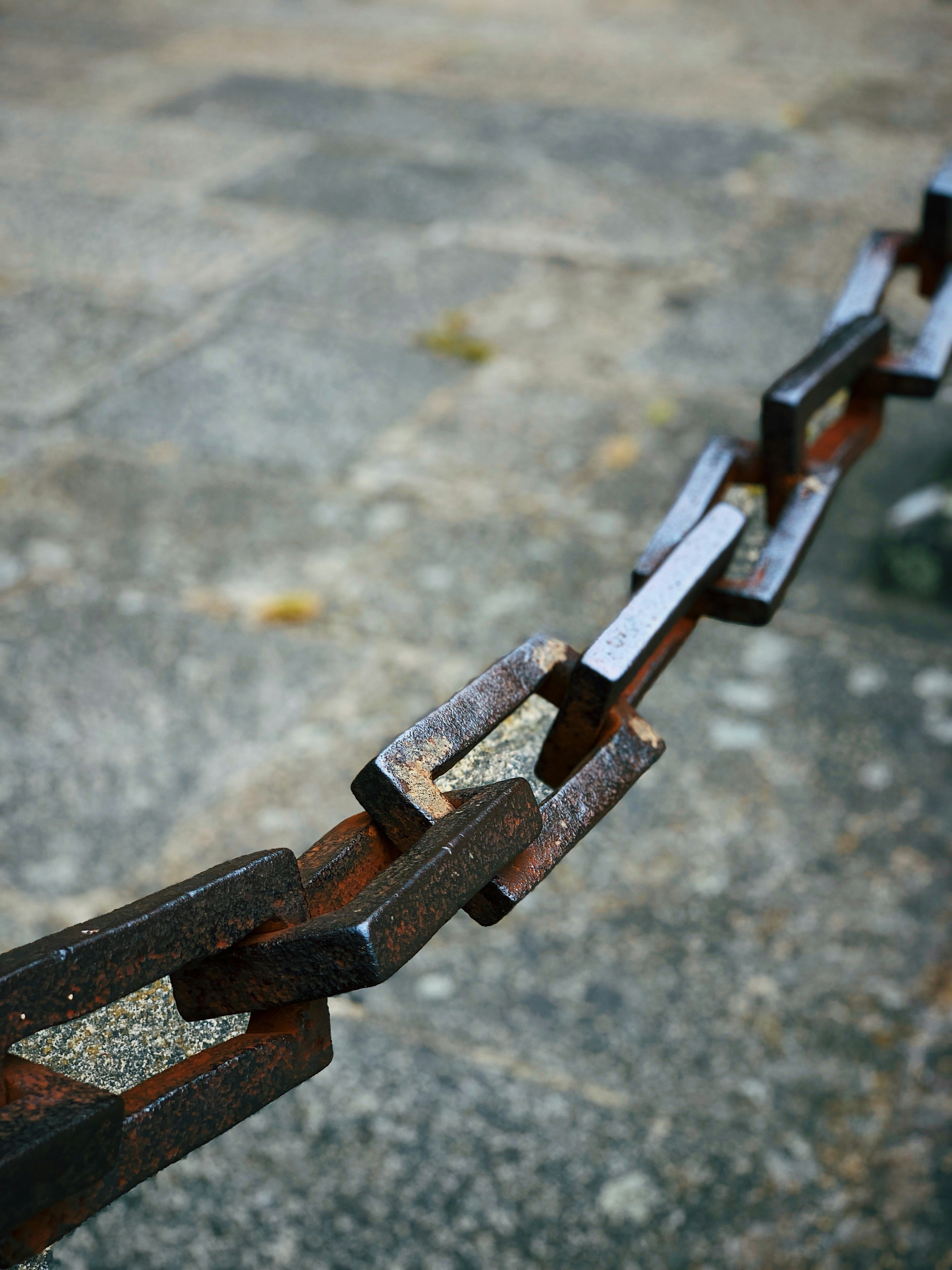 Close-up of a rusty chain link resting on a textured surface, highlighting the interplay of metal and stone.