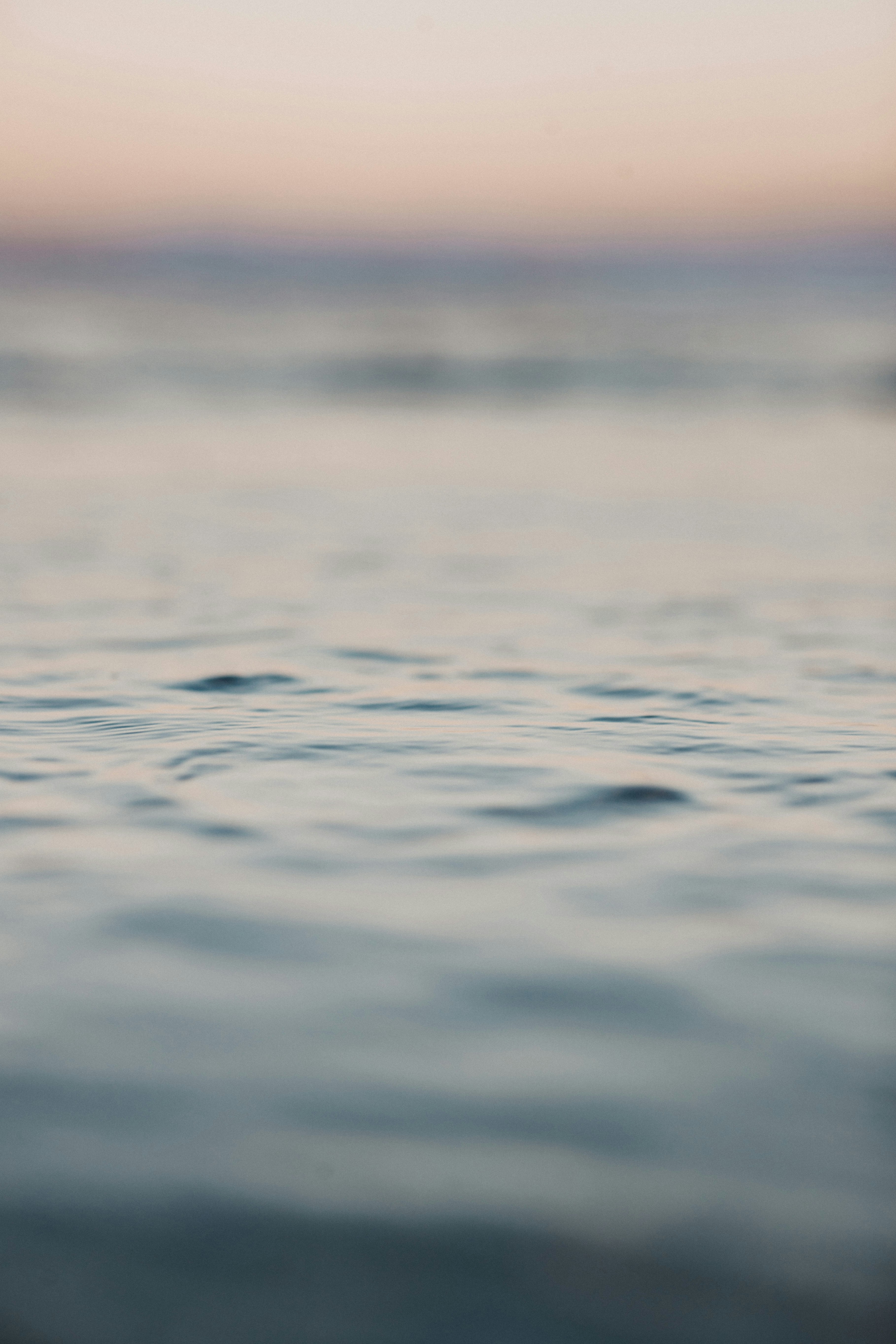 Gentle ripples of water reflecting soft hues of dawn on the horizon.