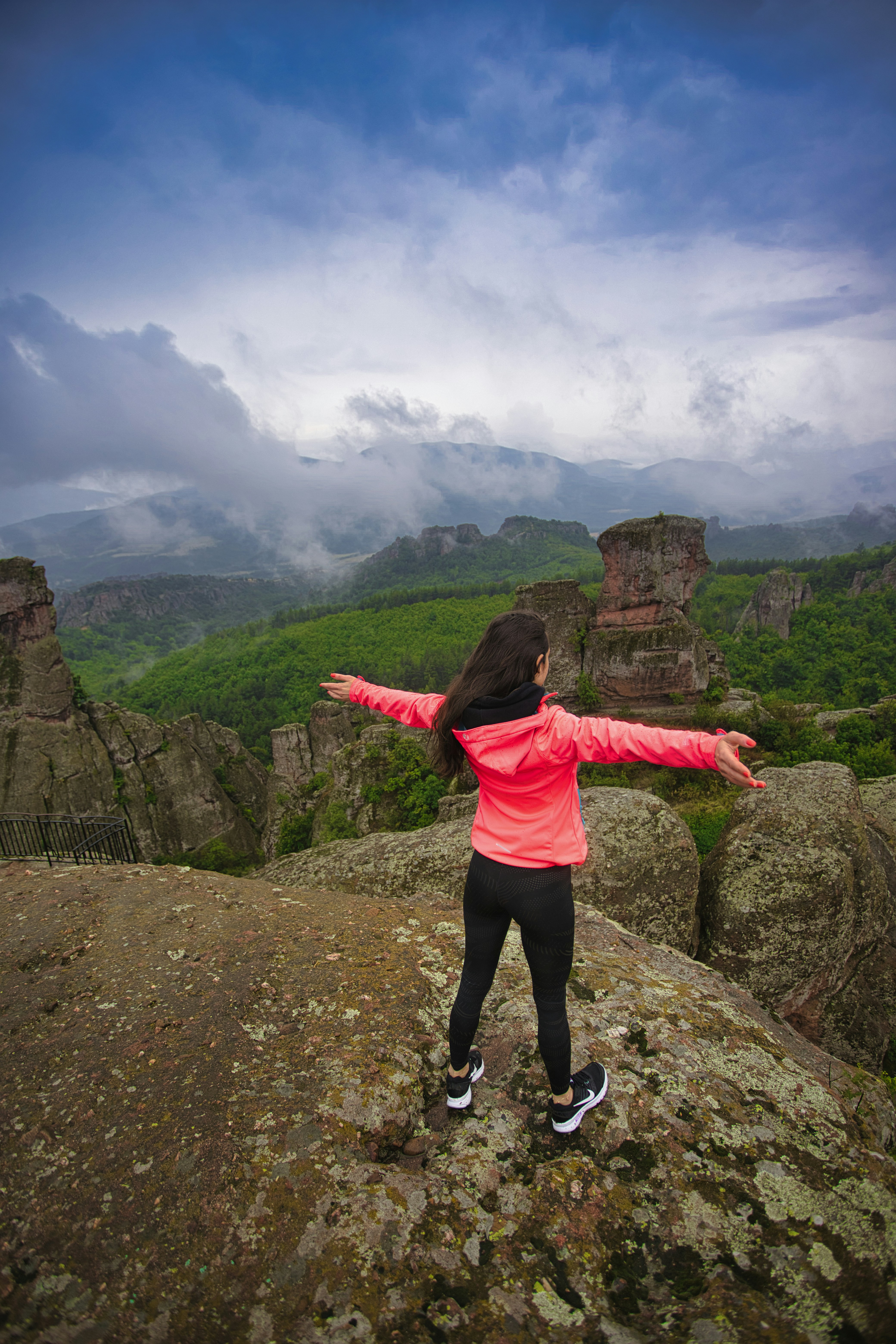 Open-Arm Summit: Woman in Coral Jacket Embracing a Vast Canyon